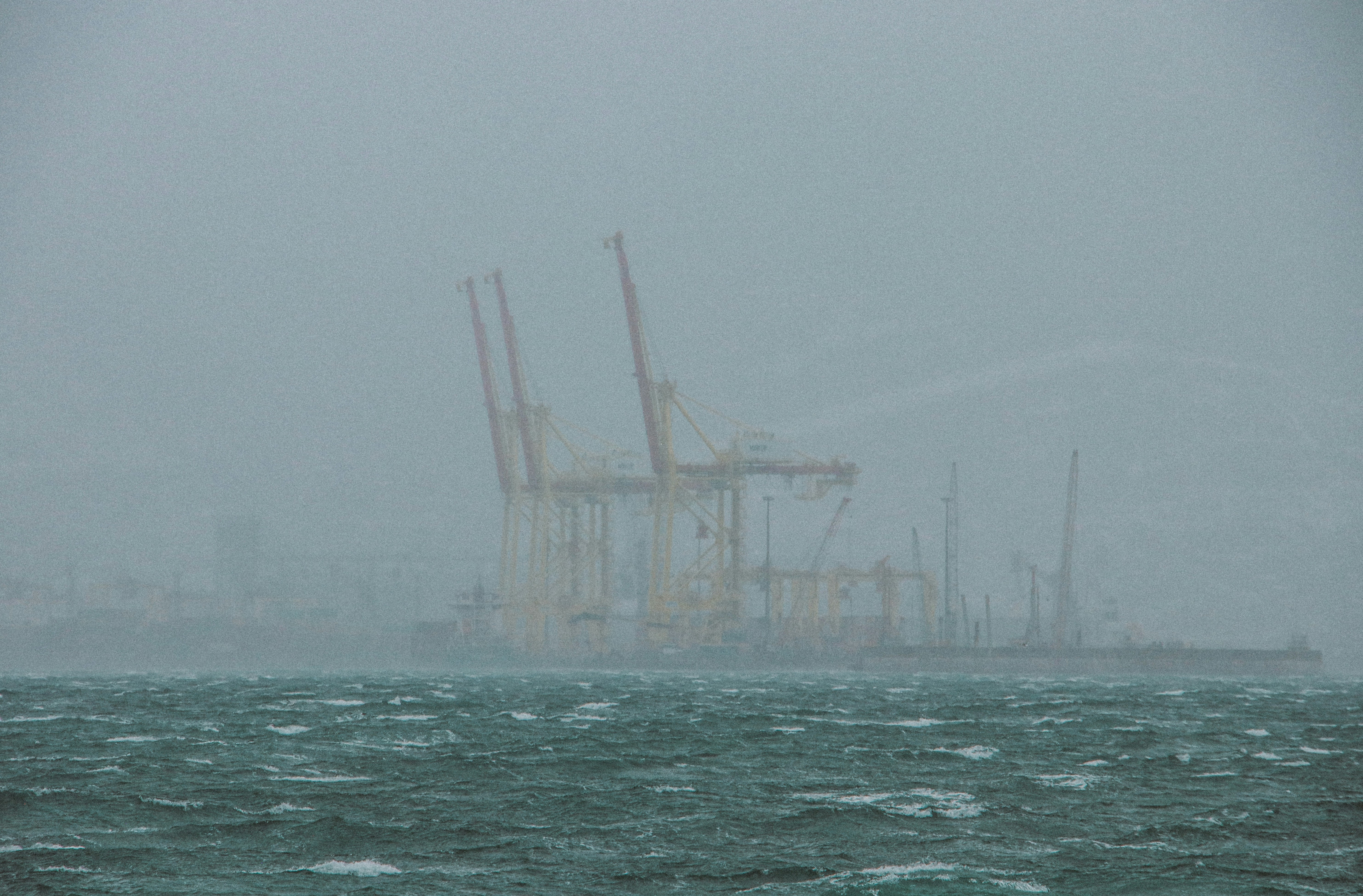 Cranes loom over a foggy harbor with choppy waters in the foreground.