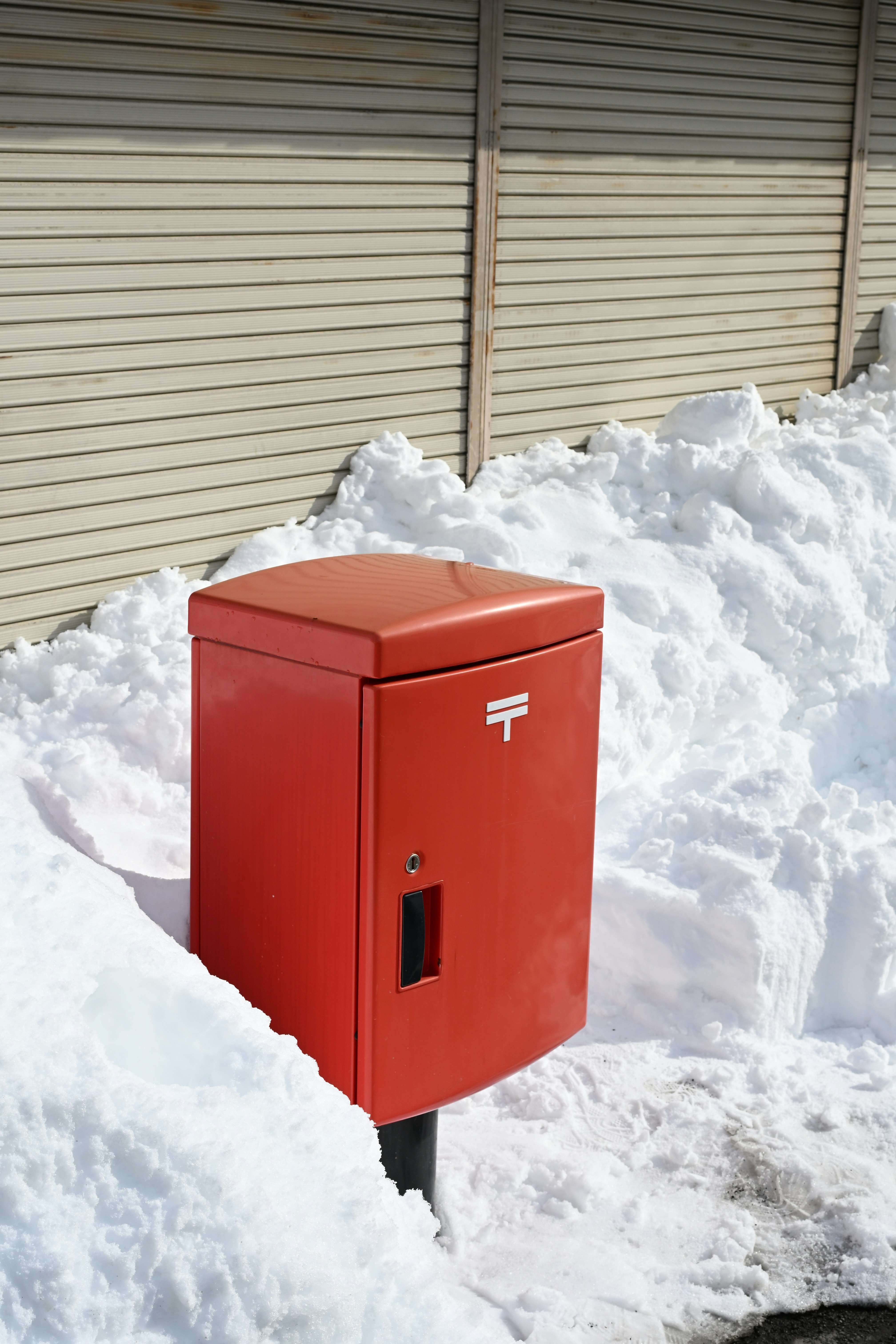 Scarlet Mailbox Rising from Snow by a Quiet Beige Wall