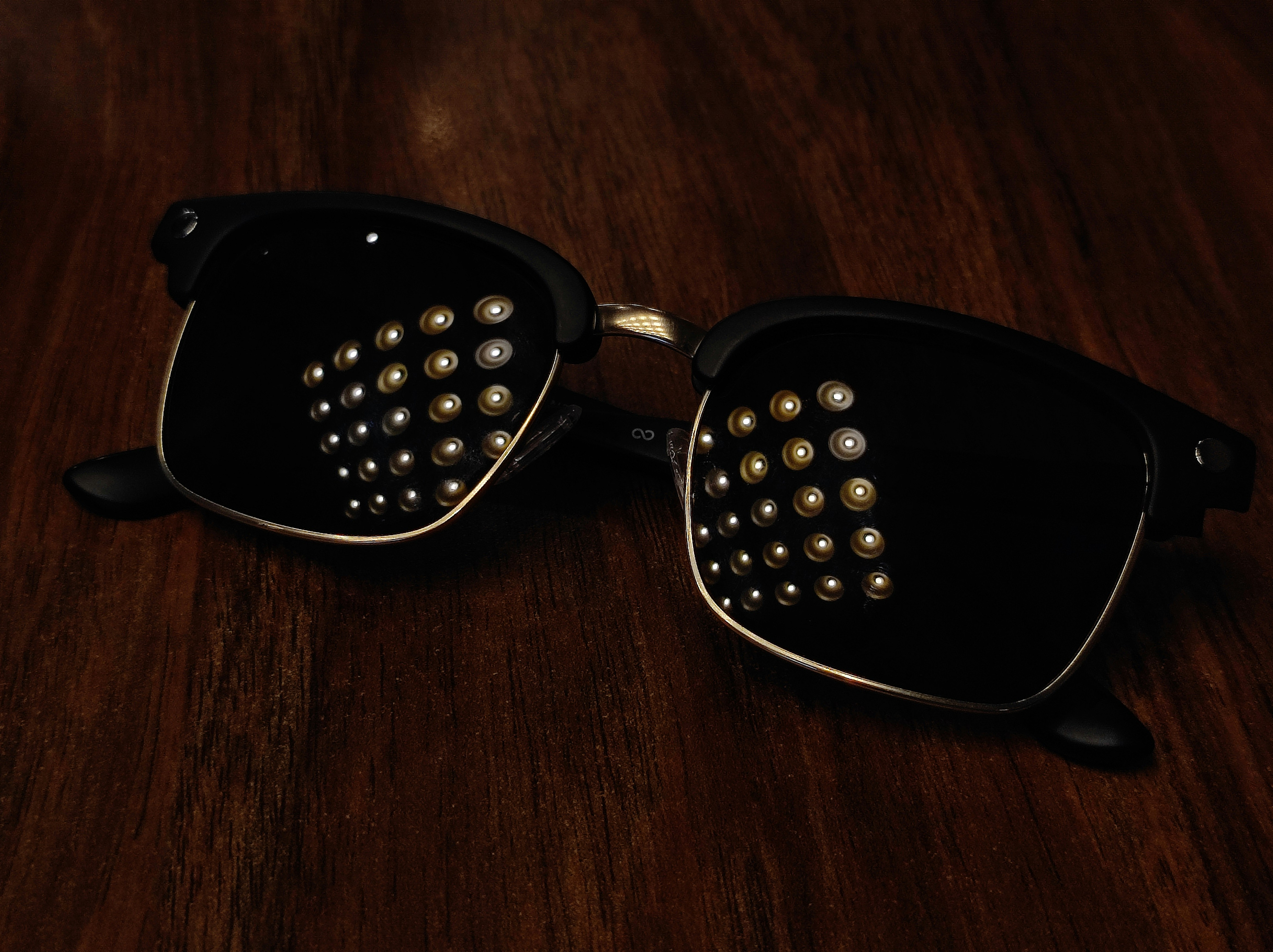 Sunglasses with studded lenses rest on a dark wooden surface, catching soft highlights.