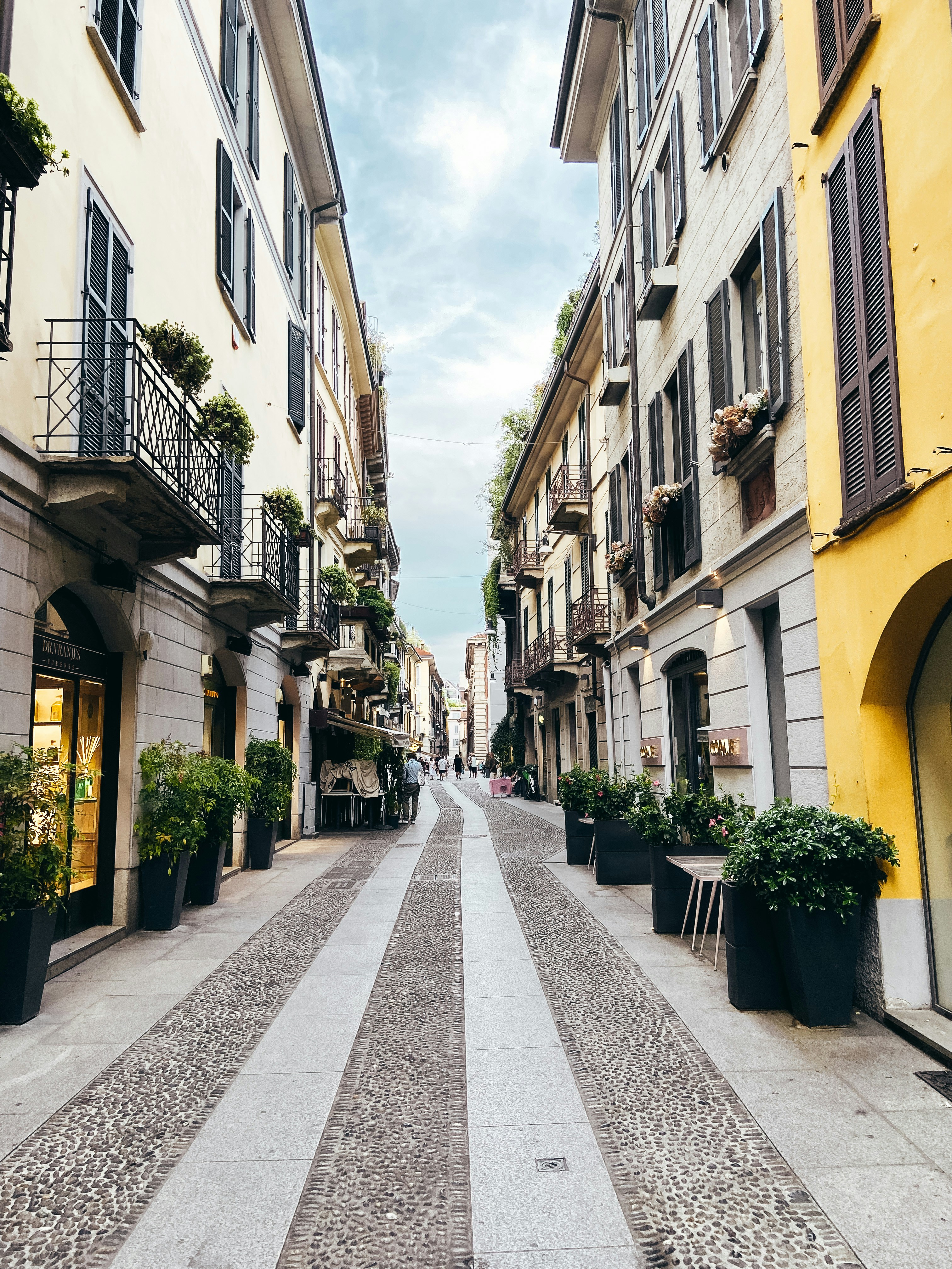 A narrow street lined with buildings and potted plants photo – Free ...