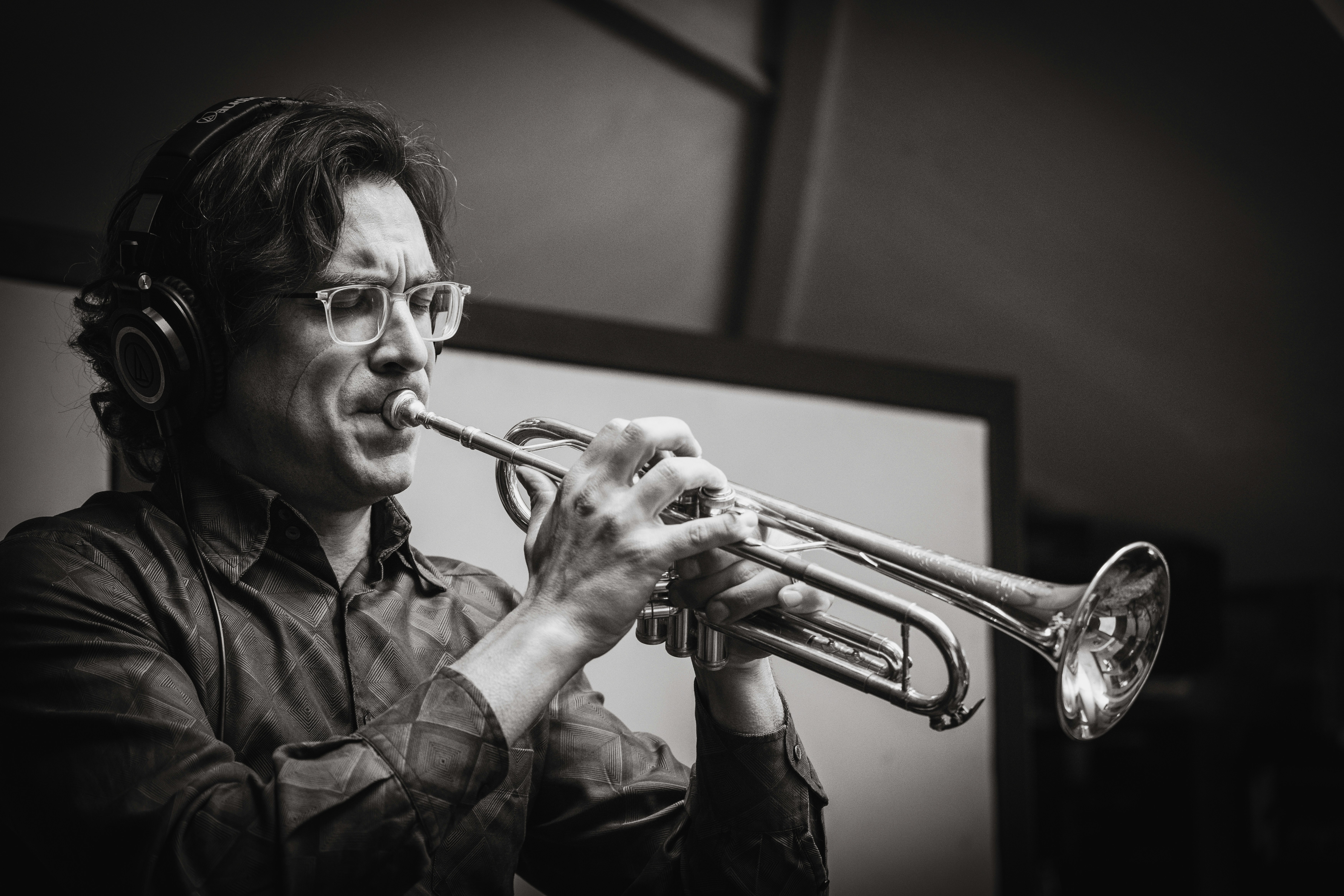 Musician playing trumpet with headphones in a black-and-white setting.