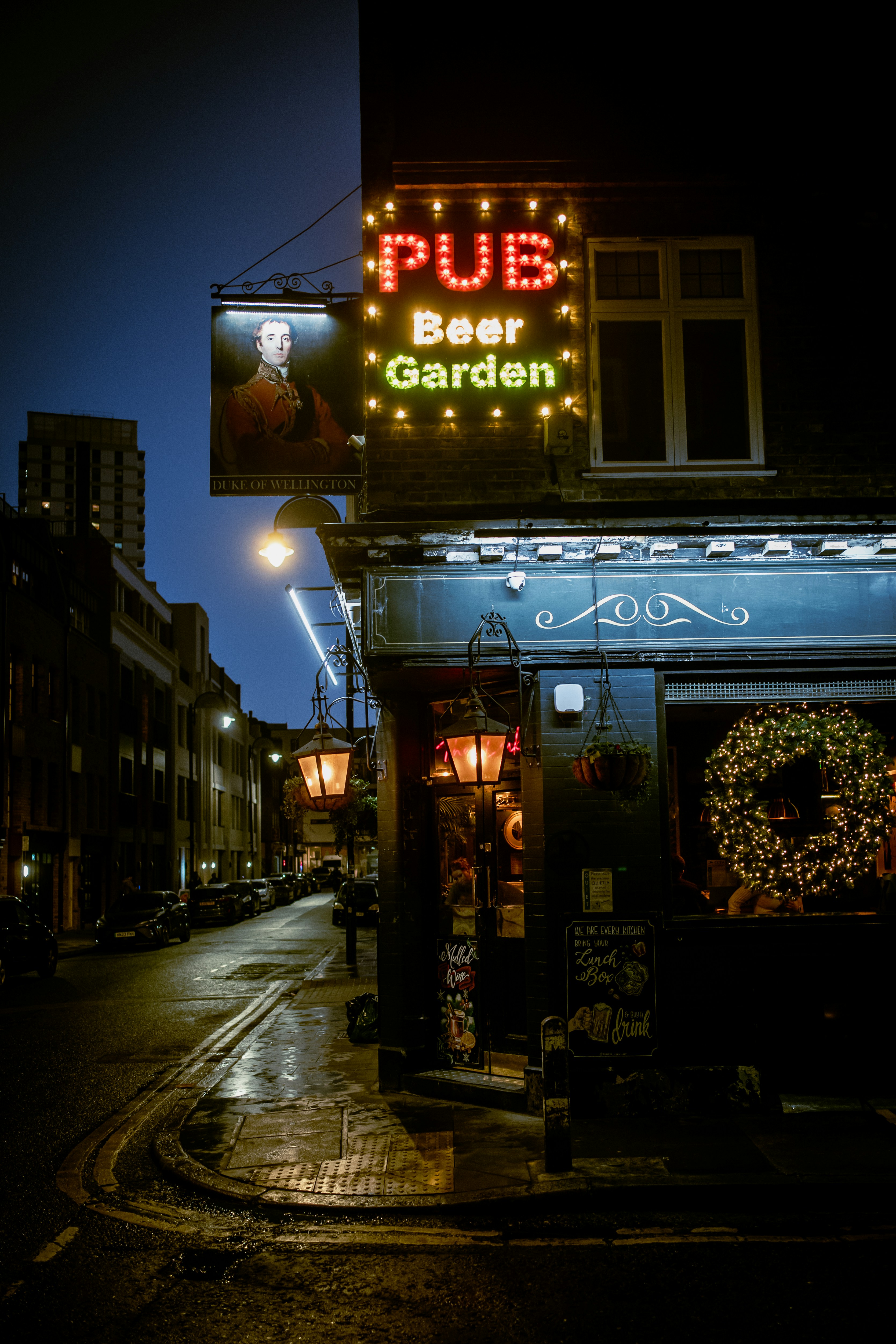 Pub entrance illuminated by colorful lights on a dimly lit street corner at dusk.