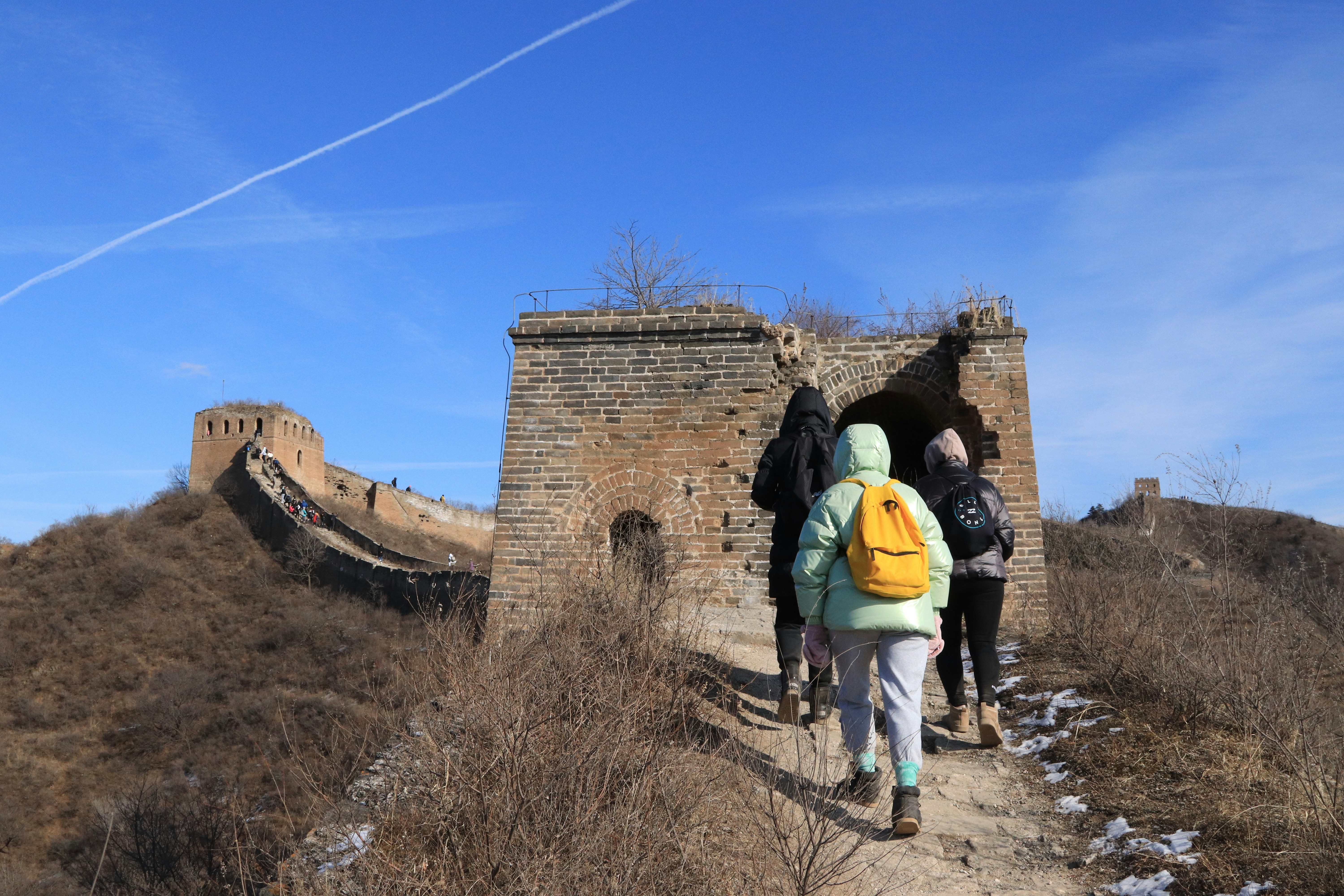 Hikers explore a rugged section of the Great Wall under a clear blue sky.