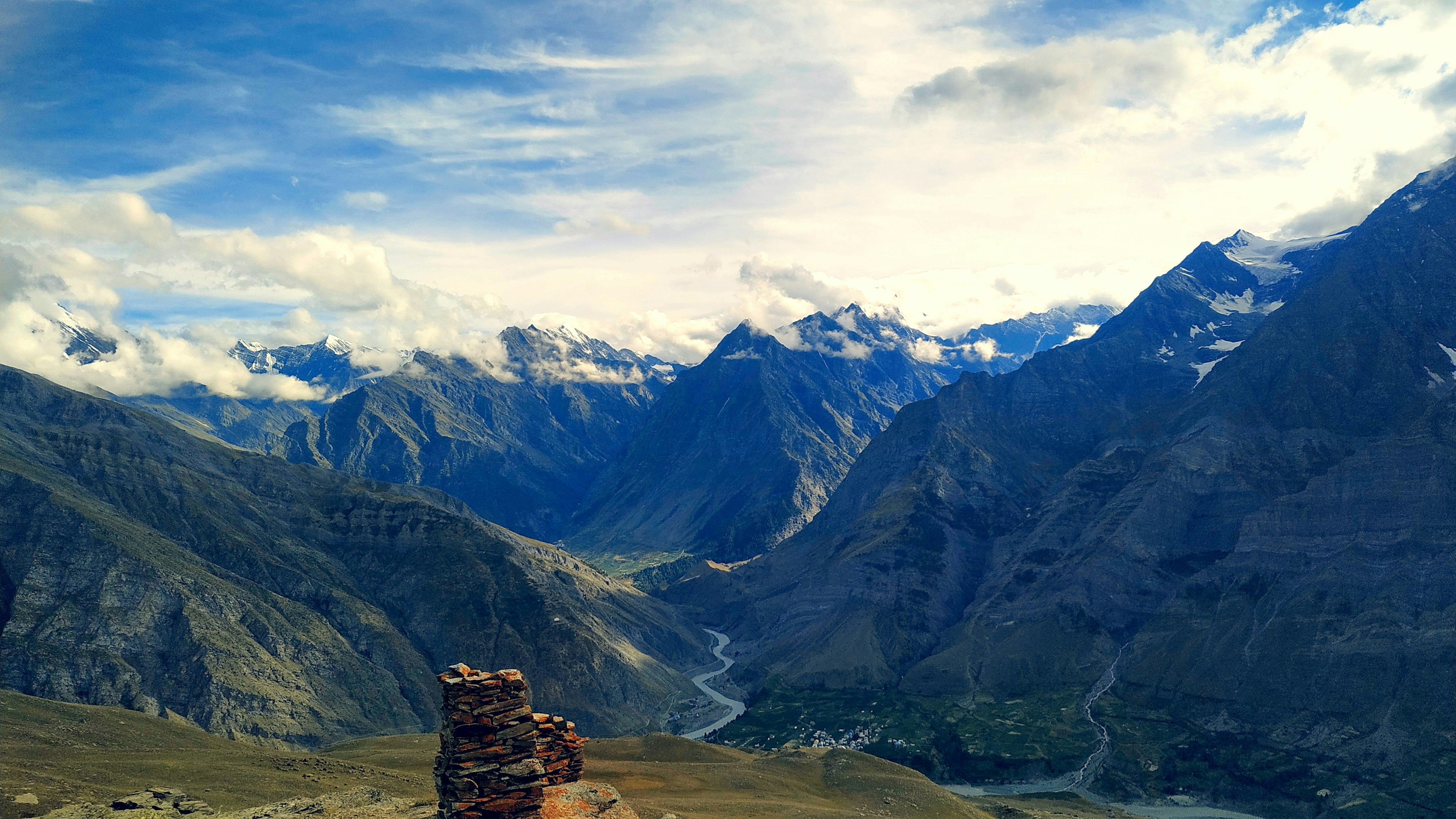 Rock cairn overlooking expansive mountain range with a winding river under a cloudy sky.