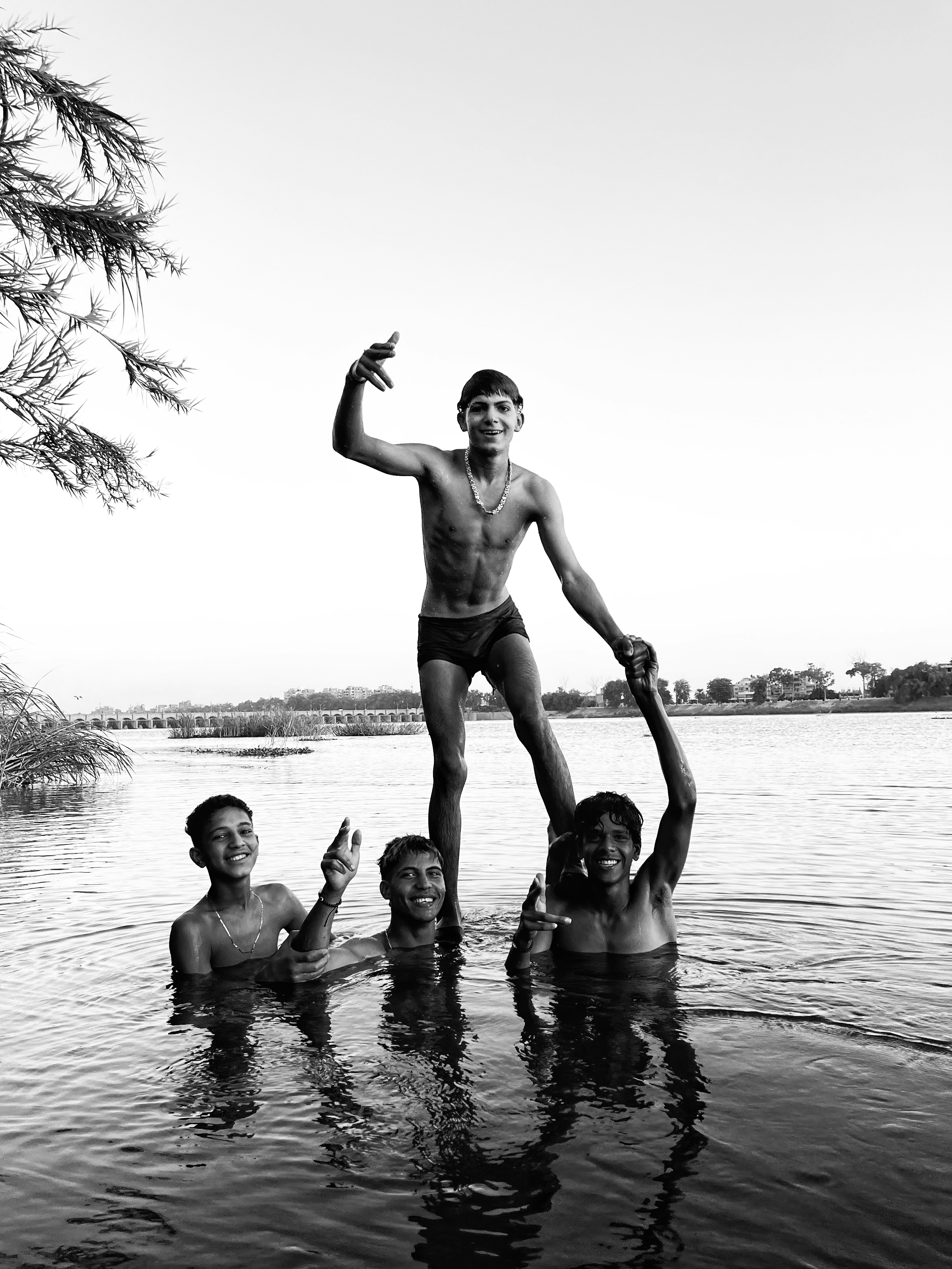 Group of four people enjoying a playful moment in a calm lake, with one person balancing on top of others.