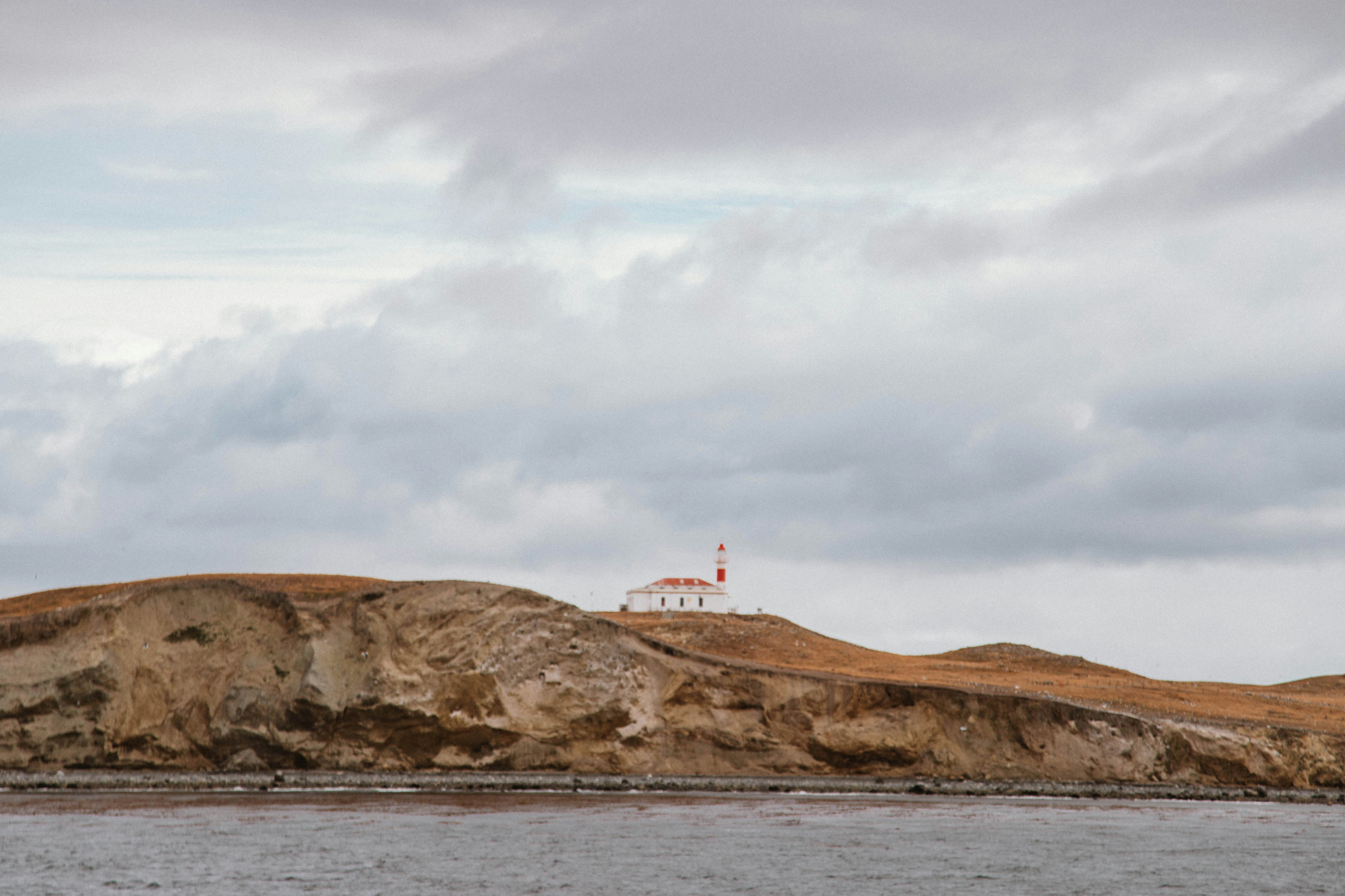 Lighthouse perched atop a rocky cliff under a cloudy sky.