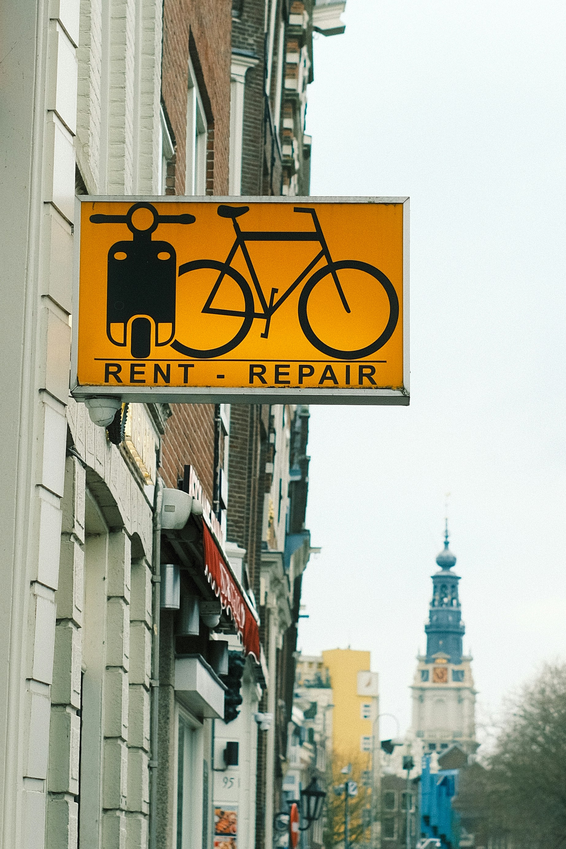 Urban Yellow Rent-Repair Sign Framing a Narrow Street with a Distant Clocktower