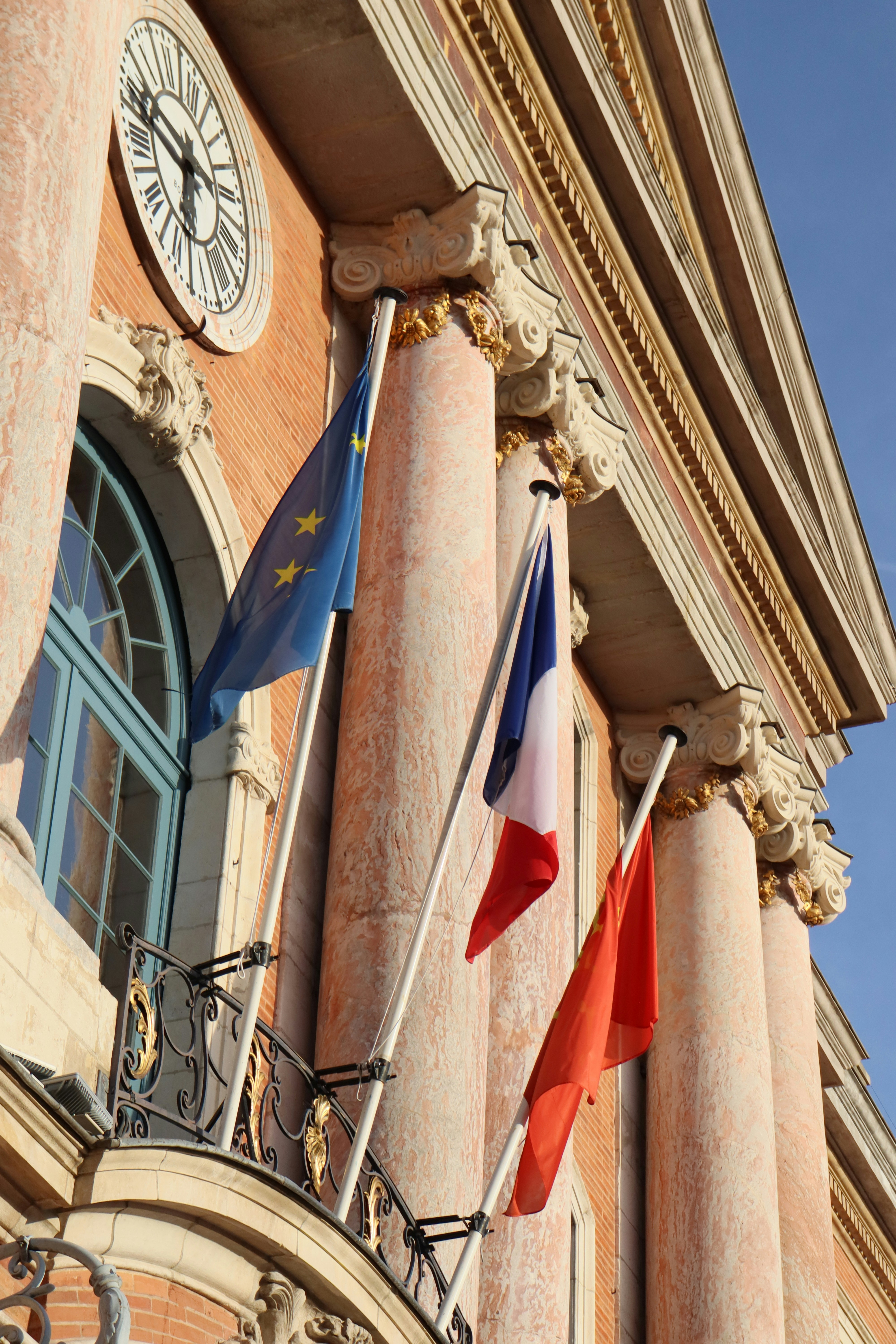 Three Flags Framing a Marble Facade Beneath a Clock