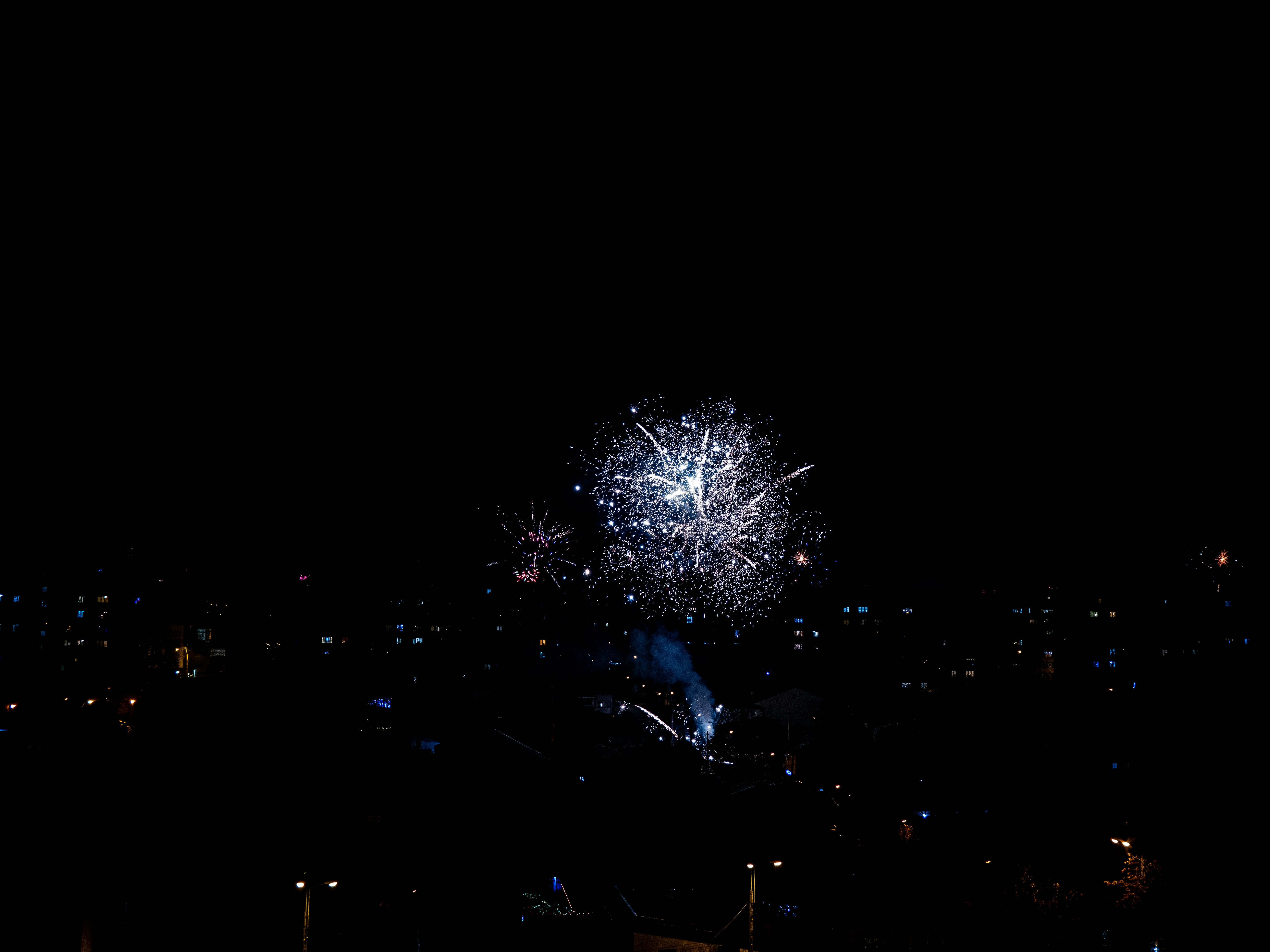 Vibrant fireworks burst in the night sky above a dimly lit cityscape.