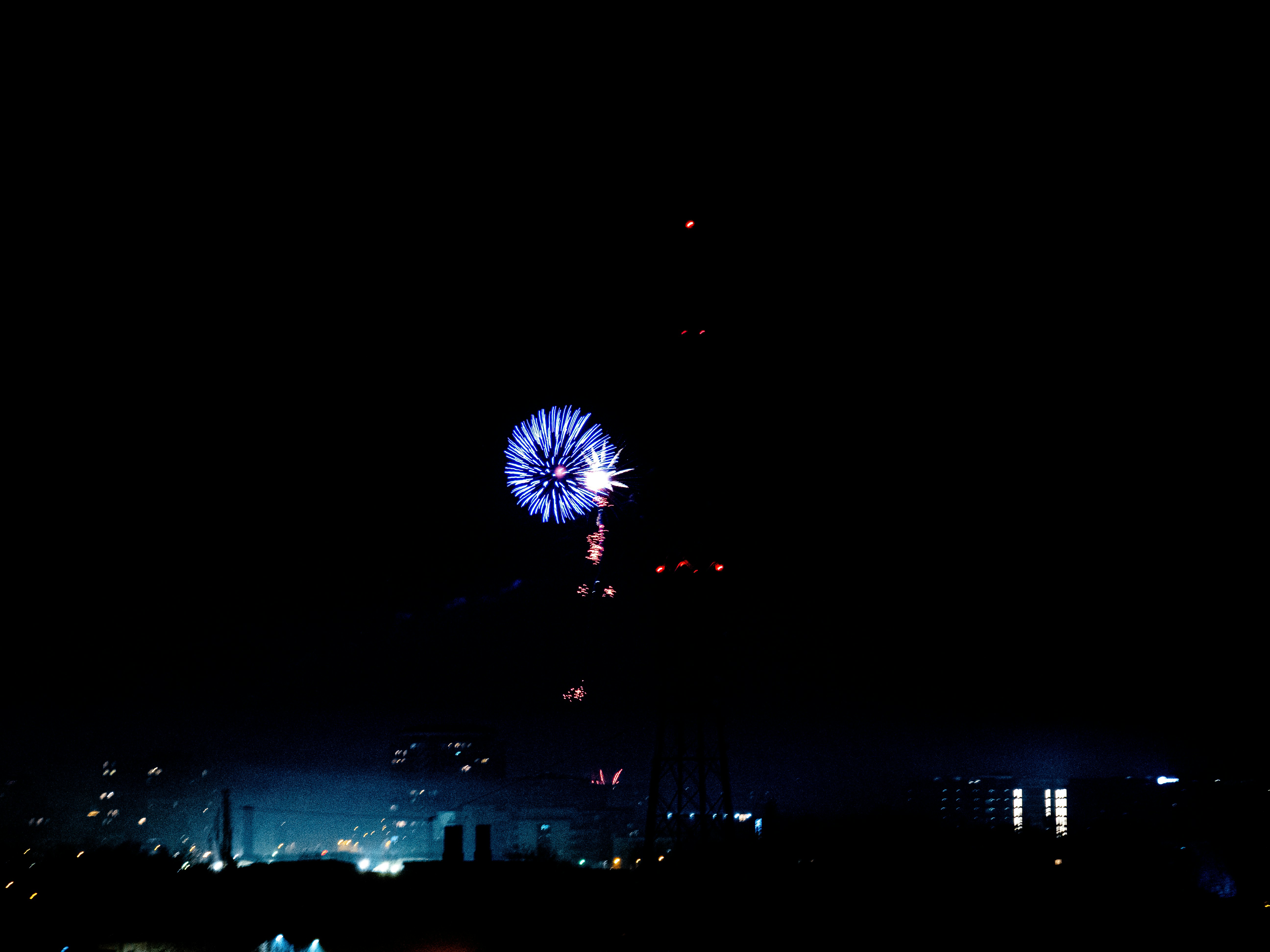 Fireworks burst in blue and purple hues against a dark city skyline, with faint building lights below.
