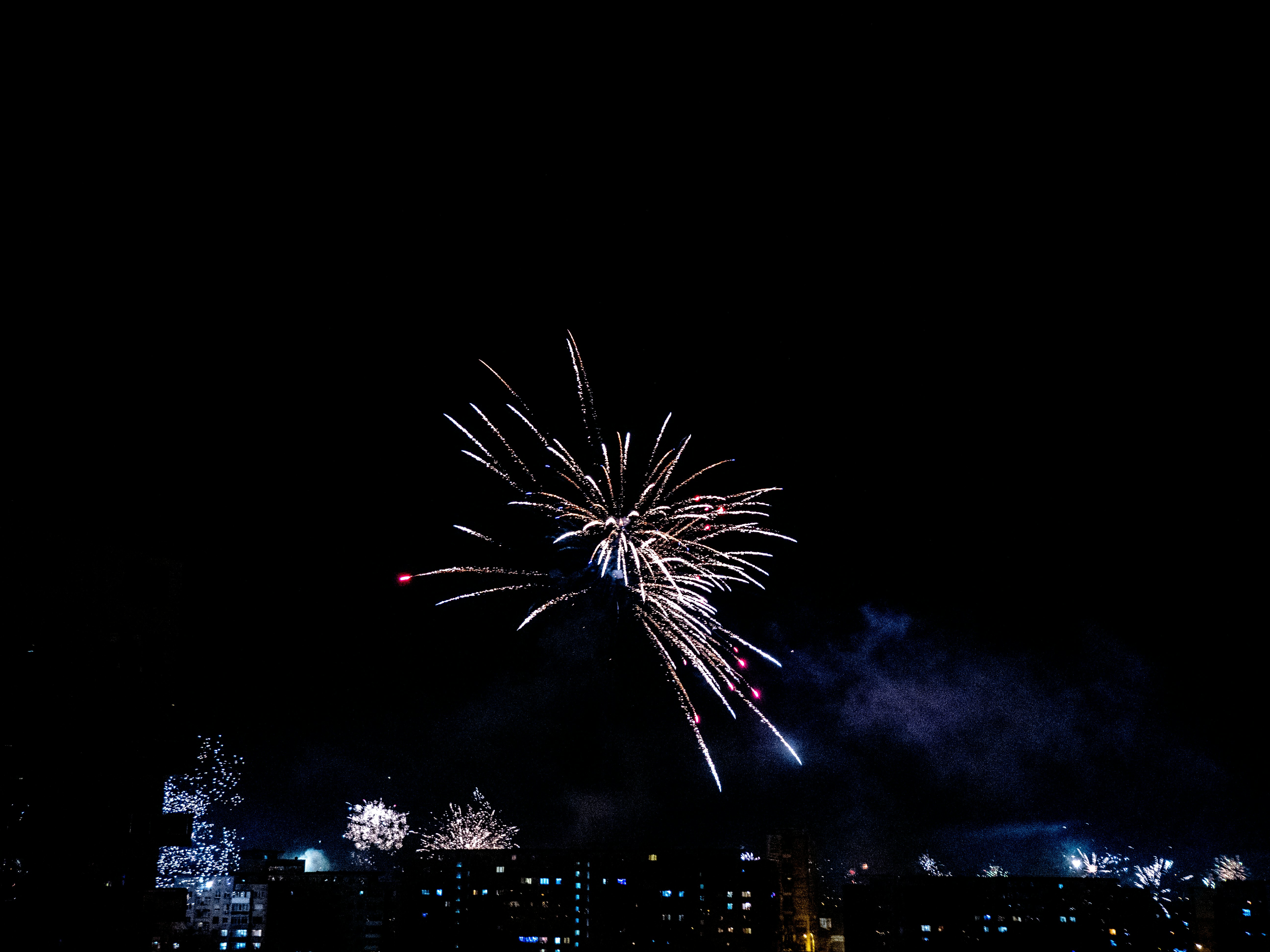 Fireworks burst in vibrant patterns above a silhouetted cityscape against the night sky.