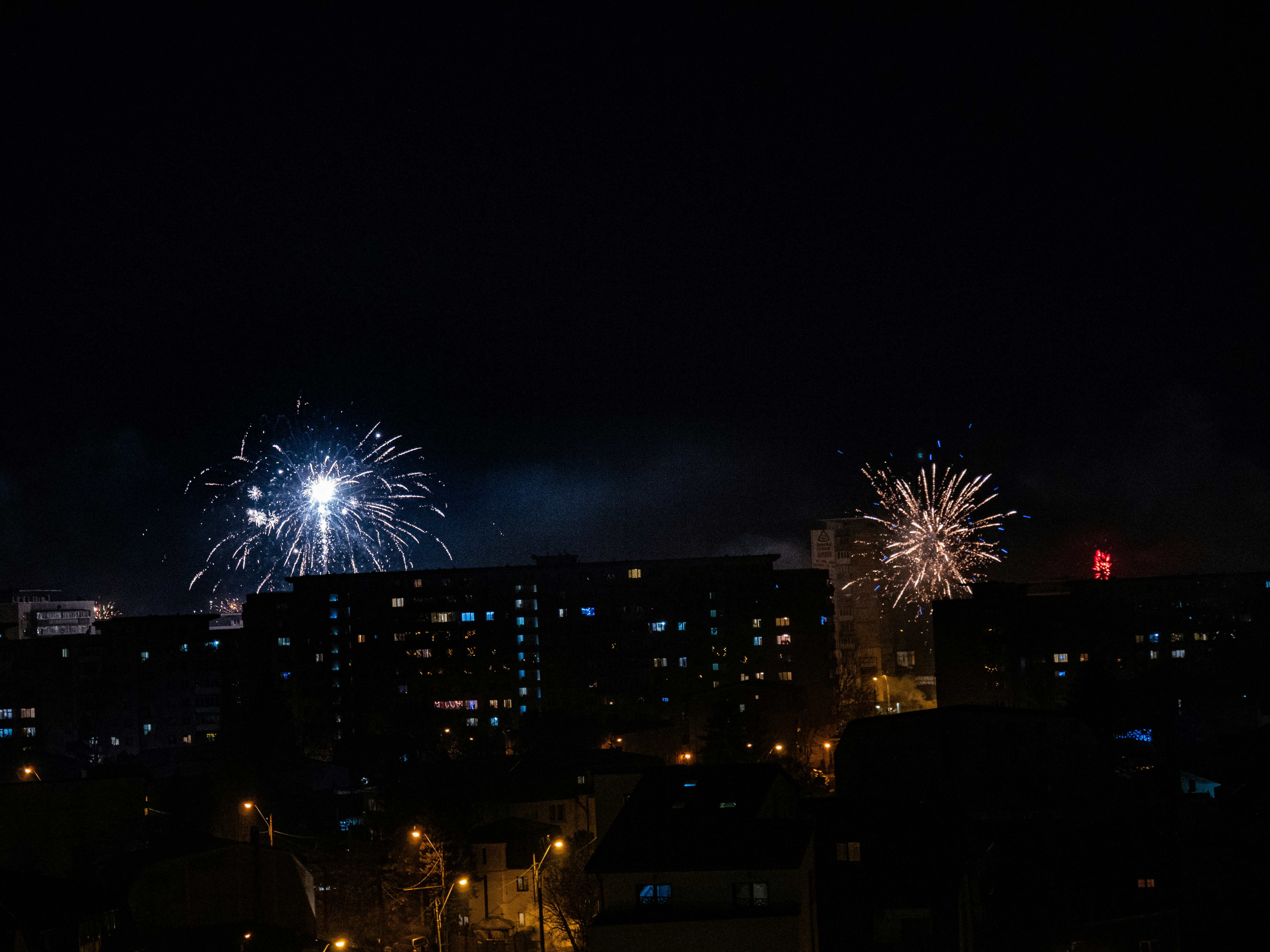 Fireworks burst in white and gold above a dark urban skyline, with streetlights illuminating the city below.