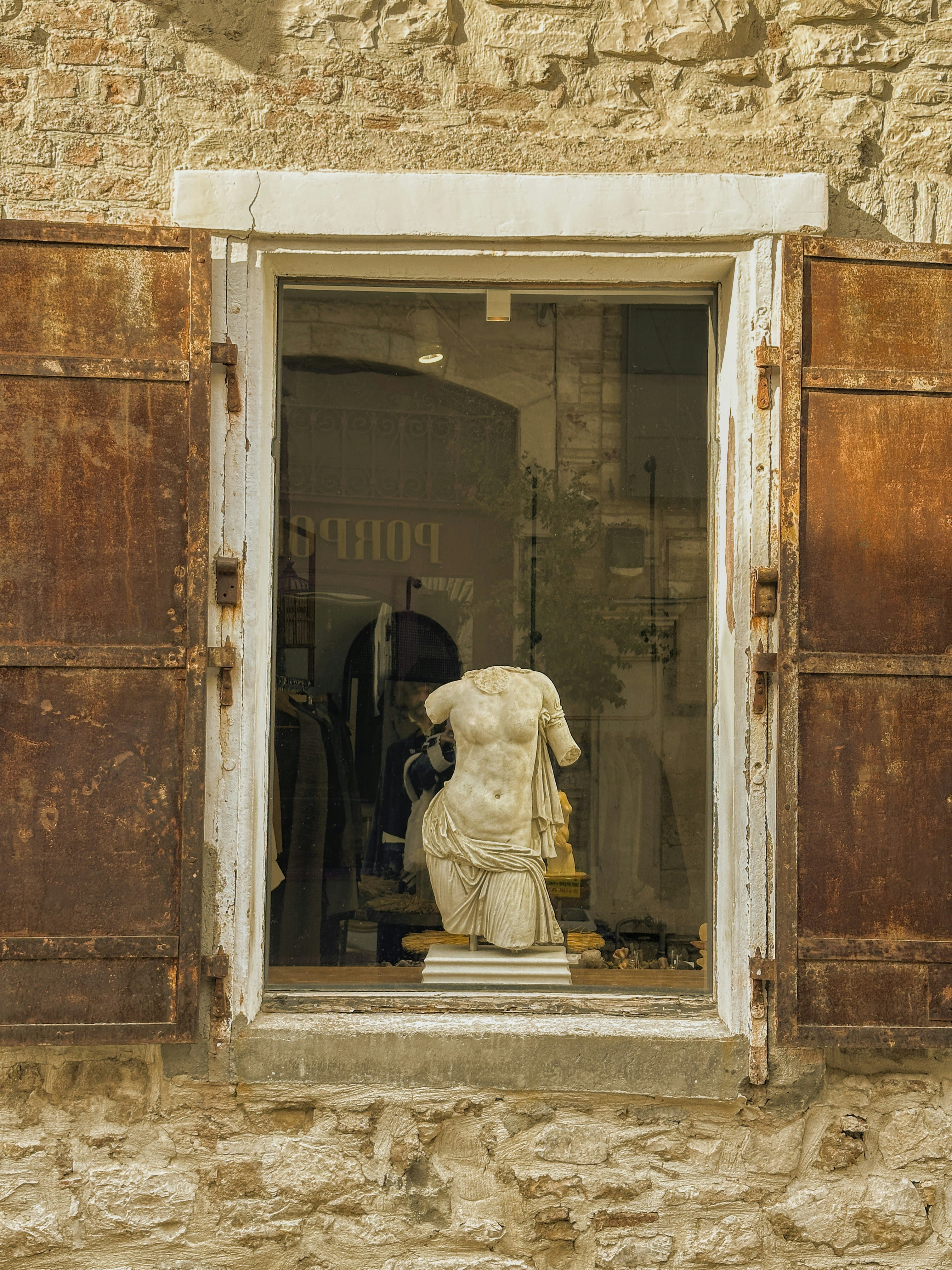 Echoes of Antiquity: a classical torso framed by rusted shutters in a sunlit shop window