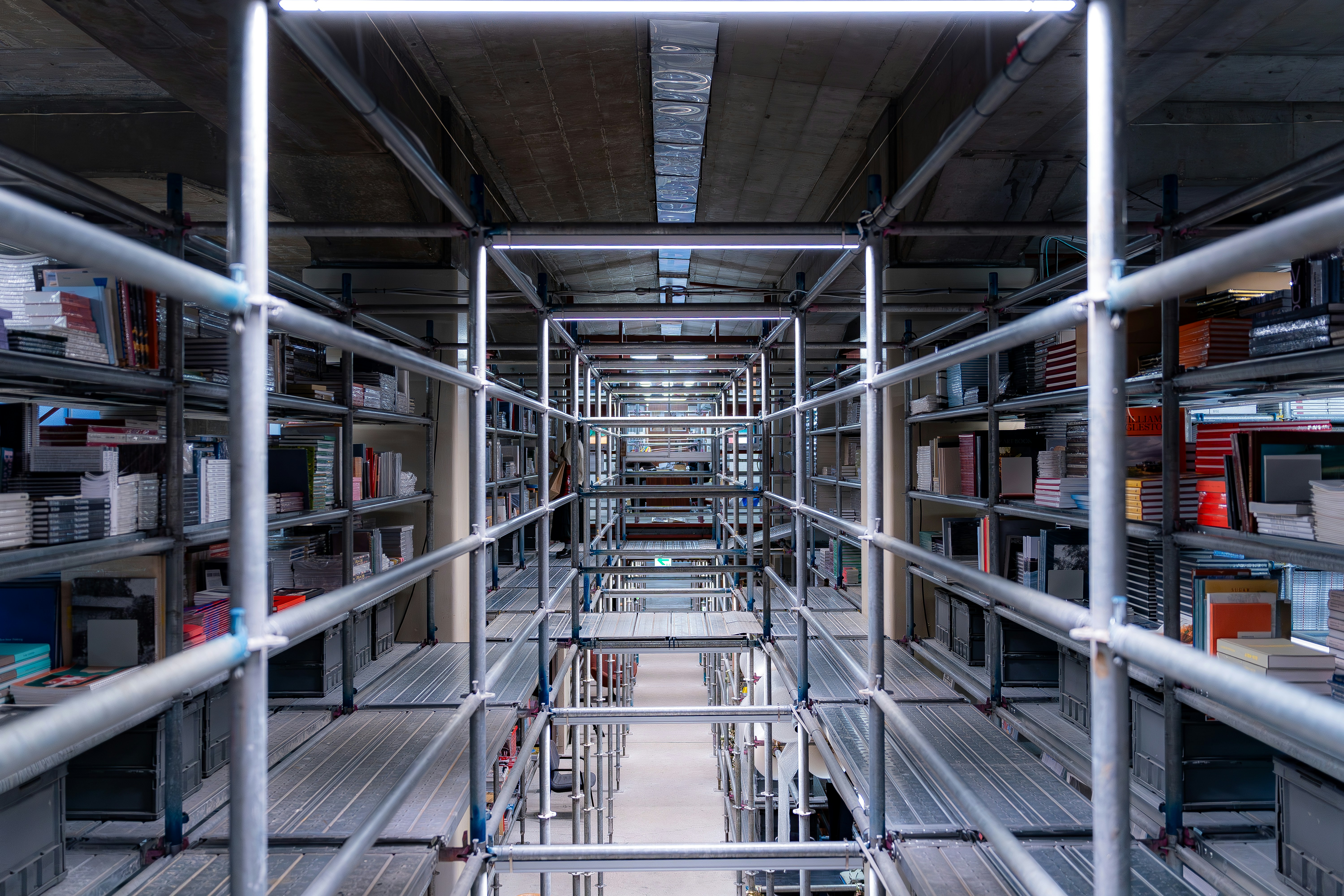 Symmetrical corridor of an industrial library with rows of books and scaffolding. Cool gray and blue tones enhance the serene atmosphere.