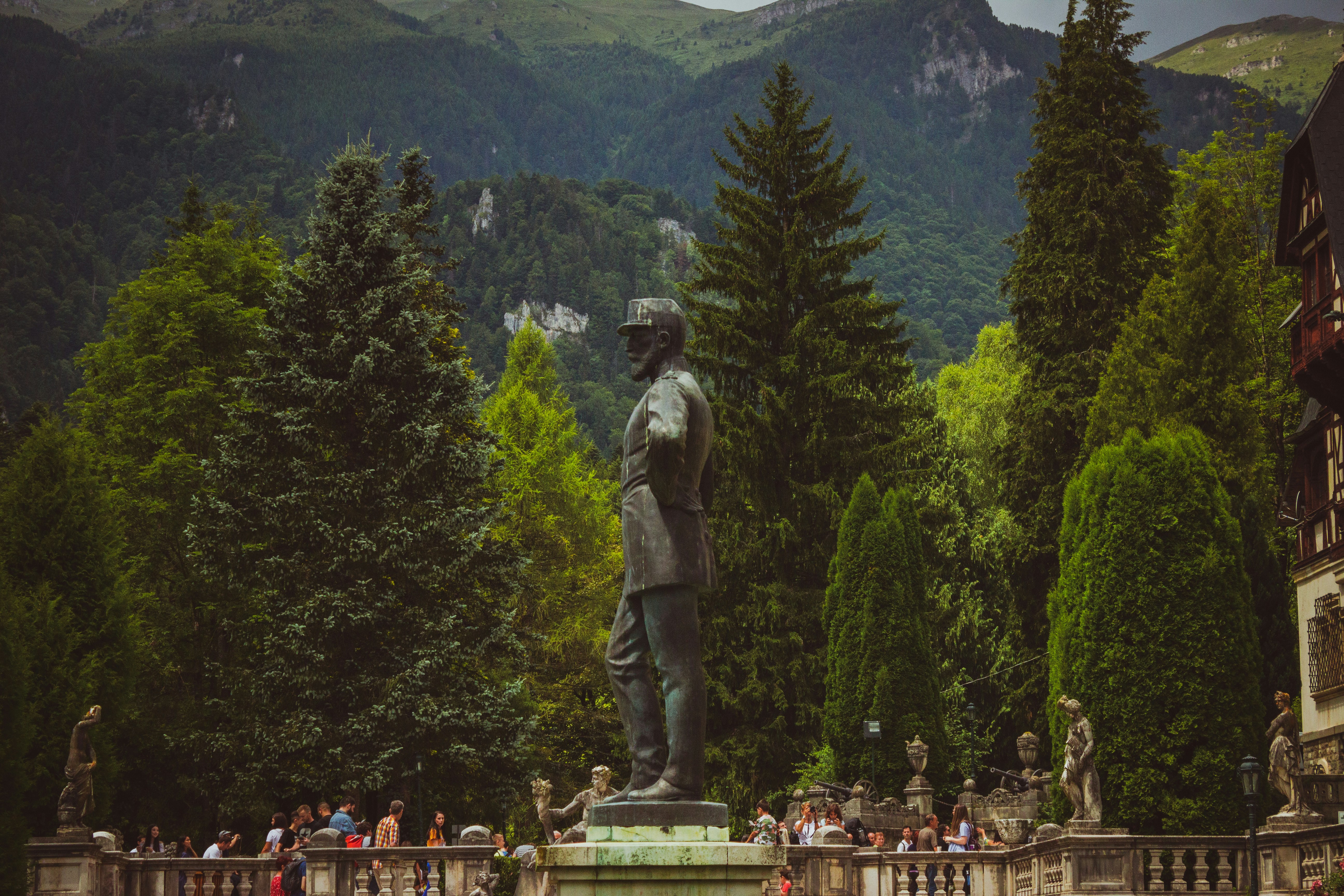 Statue stands tall among lush greenery with mountainous backdrop under overcast skies.