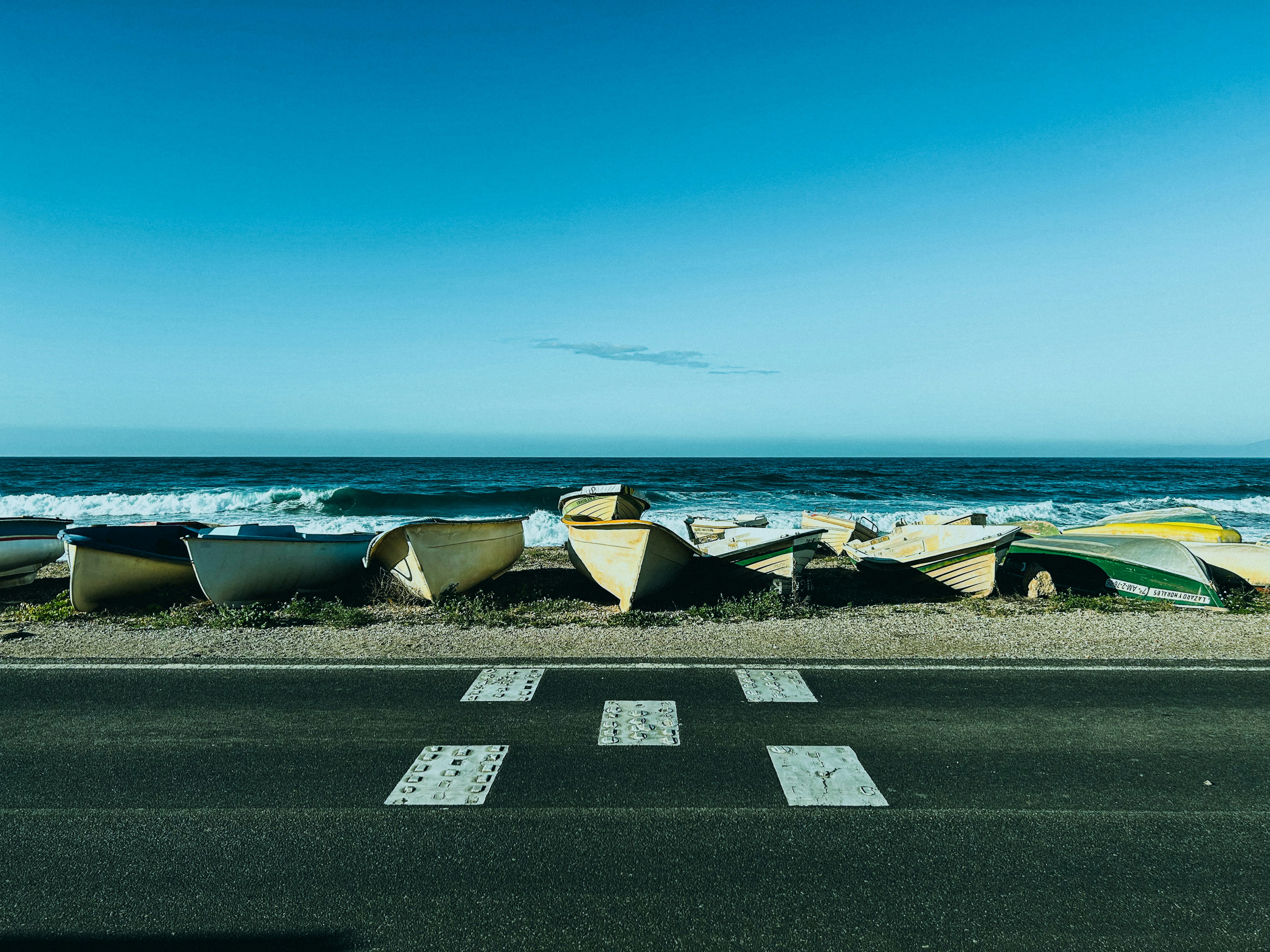 Colorful canoes lined up beside a seaside road with waves crashing in the background.