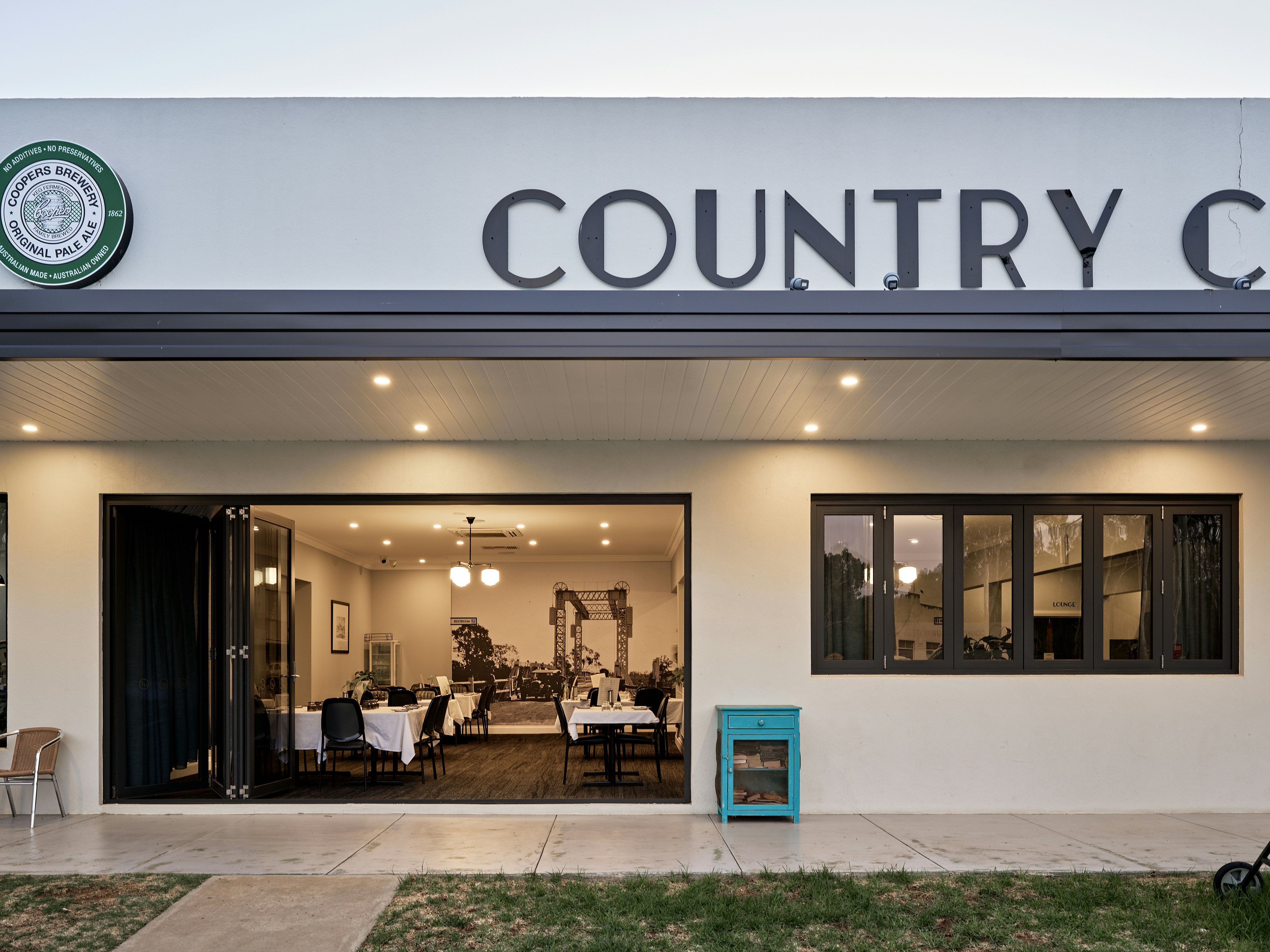 Country club exterior with warm interior lighting and a turquoise cabinet accentuating the neutral facade.