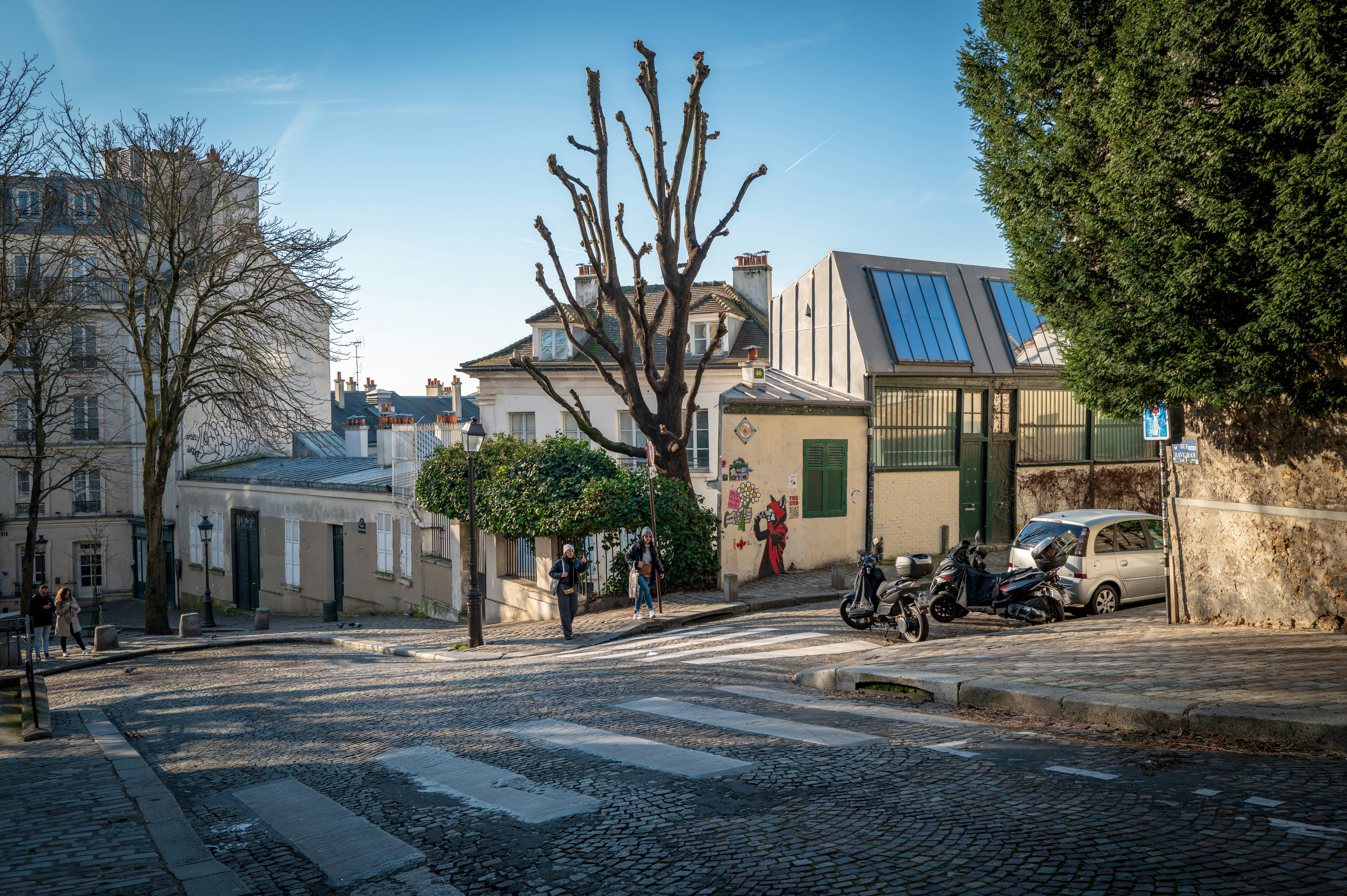 Quiet street in Bordeaux: bare trees, sunlit cobblestones and a cyclist paused near a pale-yellow shop