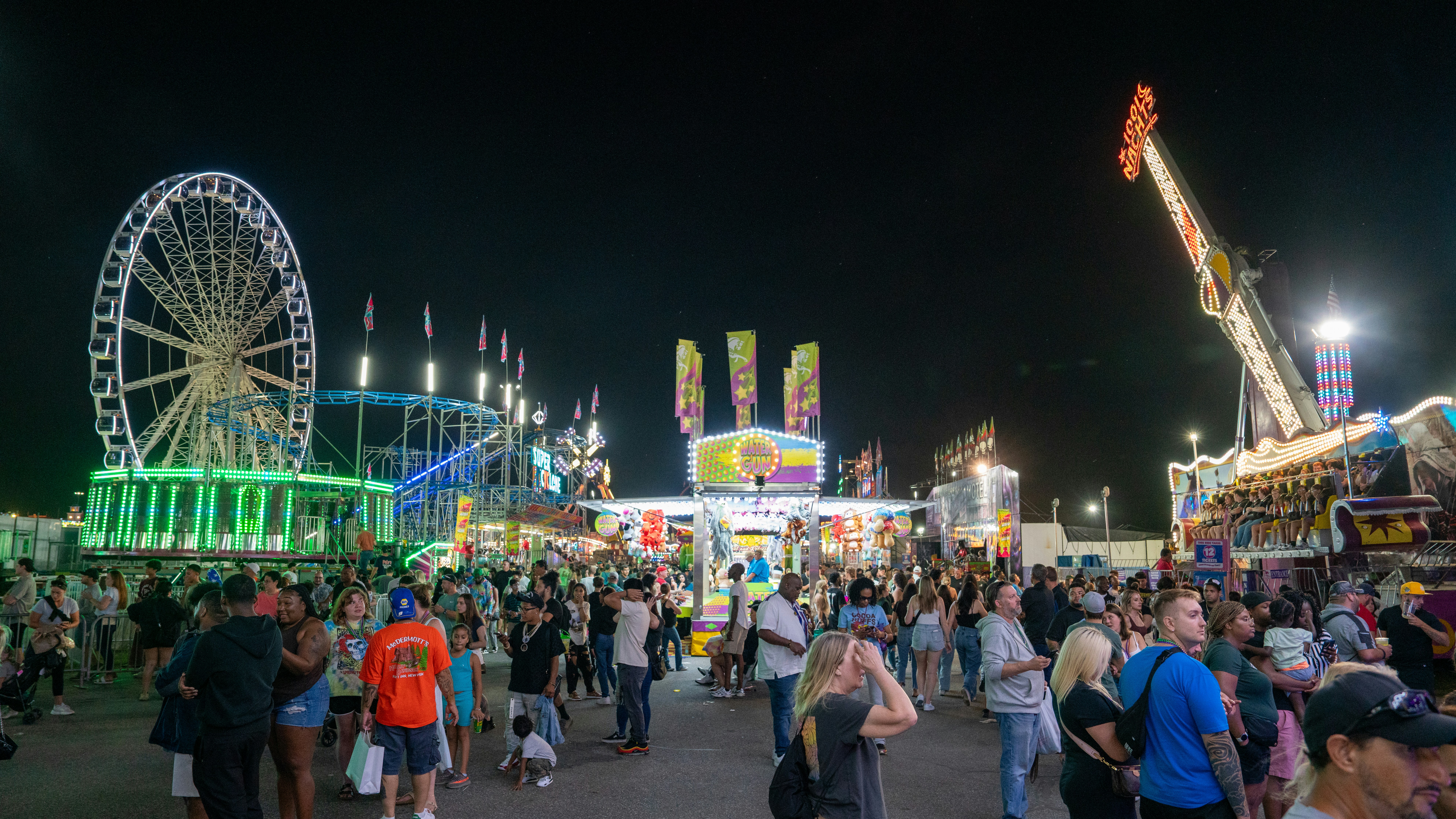 Bustling carnival scene with a glowing Ferris wheel and vibrant amusement rides under a starless sky.