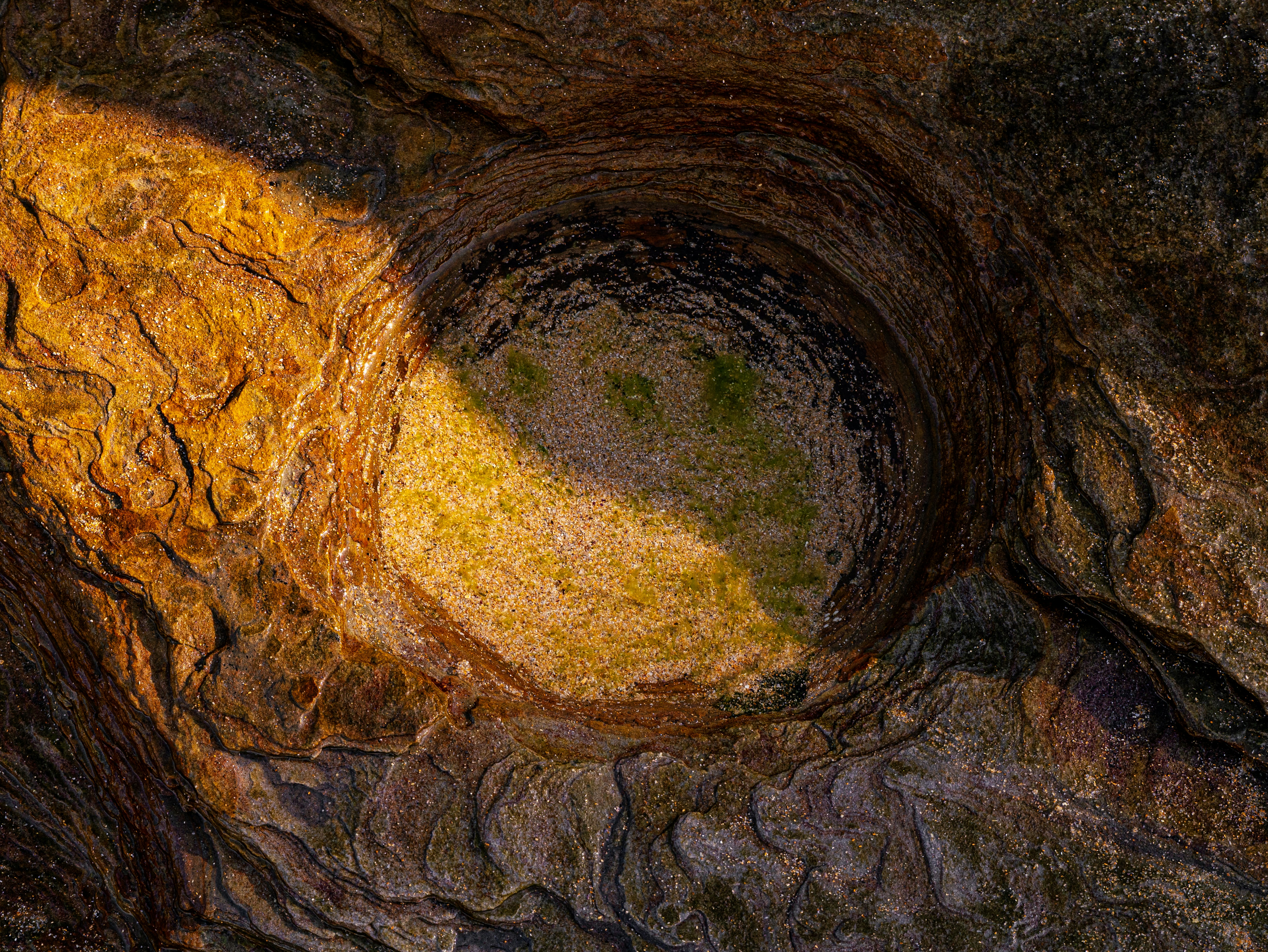 Circular rock depression bathed in warm sunlight, revealing intricate textures and earthy hues.
