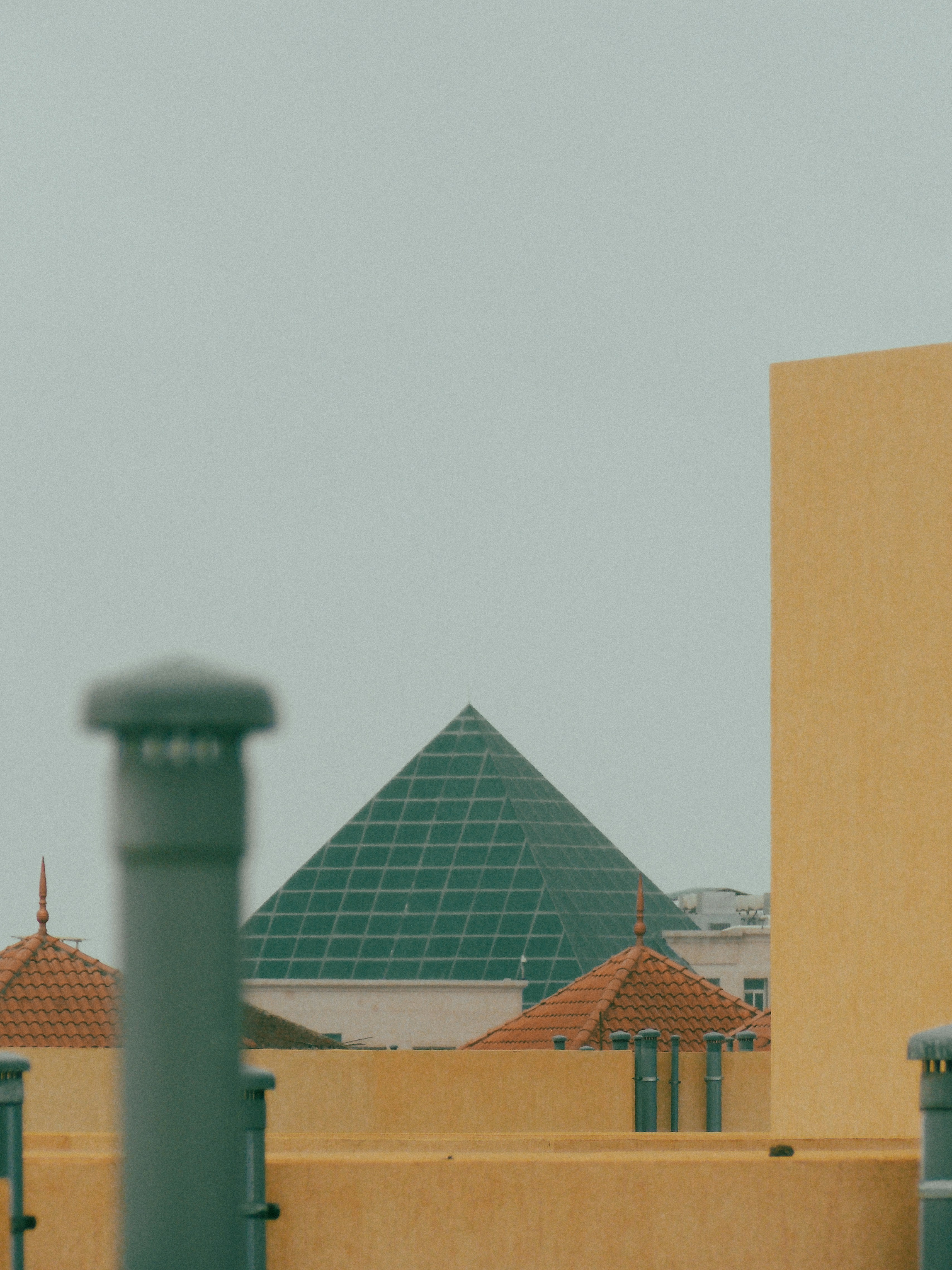 Modern pyramid structure framed by urban rooftops and muted sky.