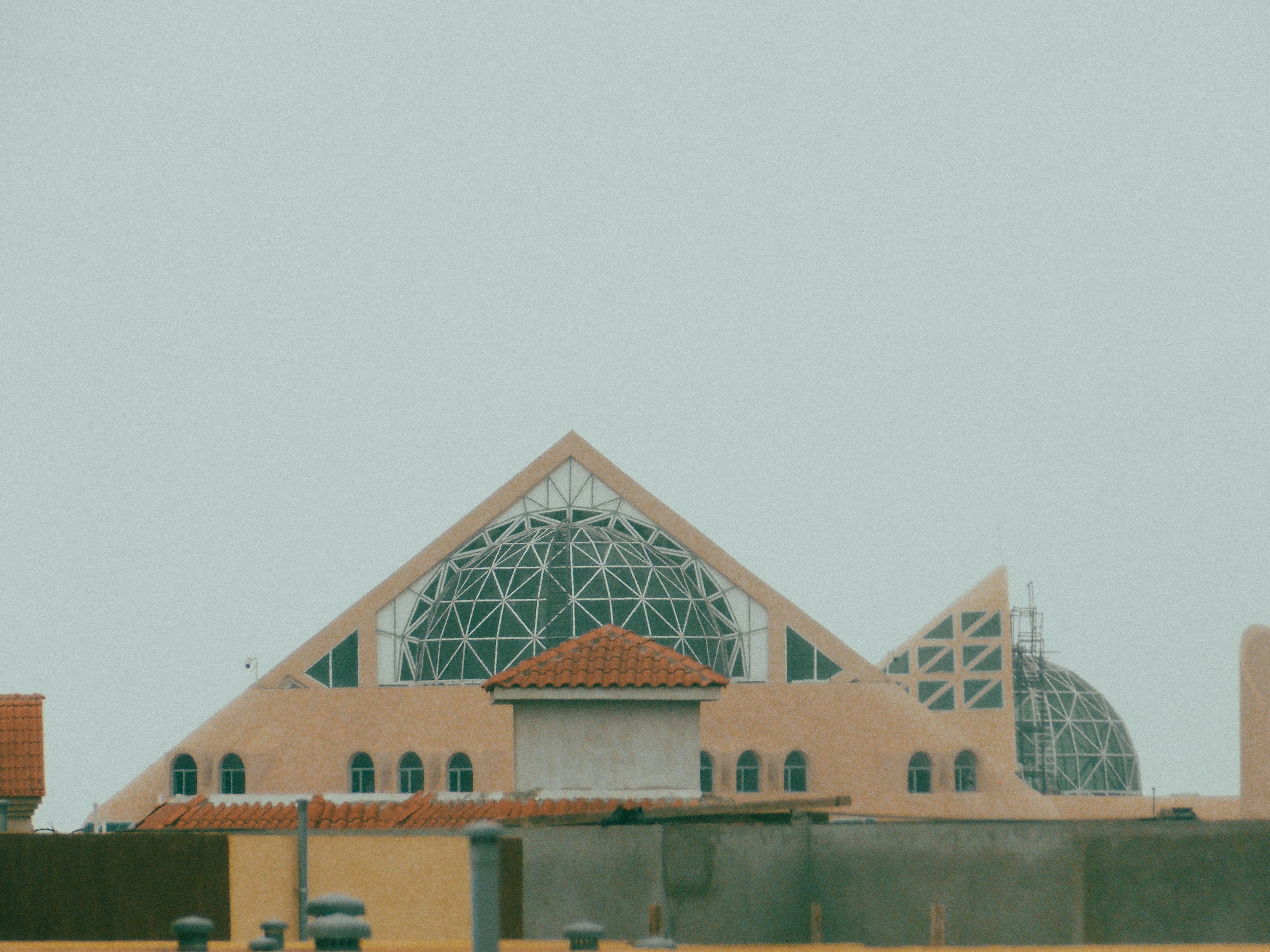 Modern building with geometric shapes and glass domes against a muted sky.
