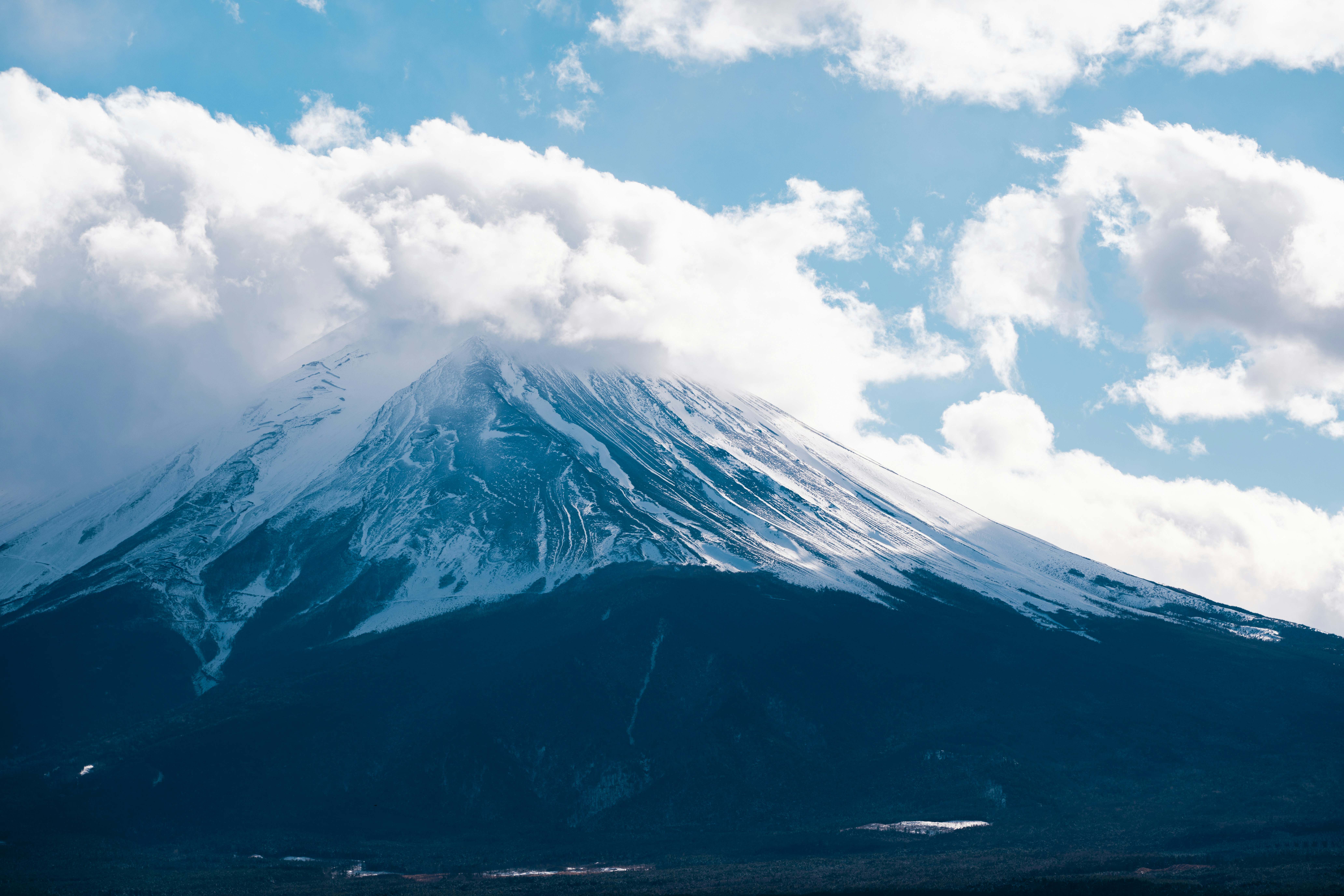 Snow-capped mountain peak enveloped by clouds against a bright blue sky.
