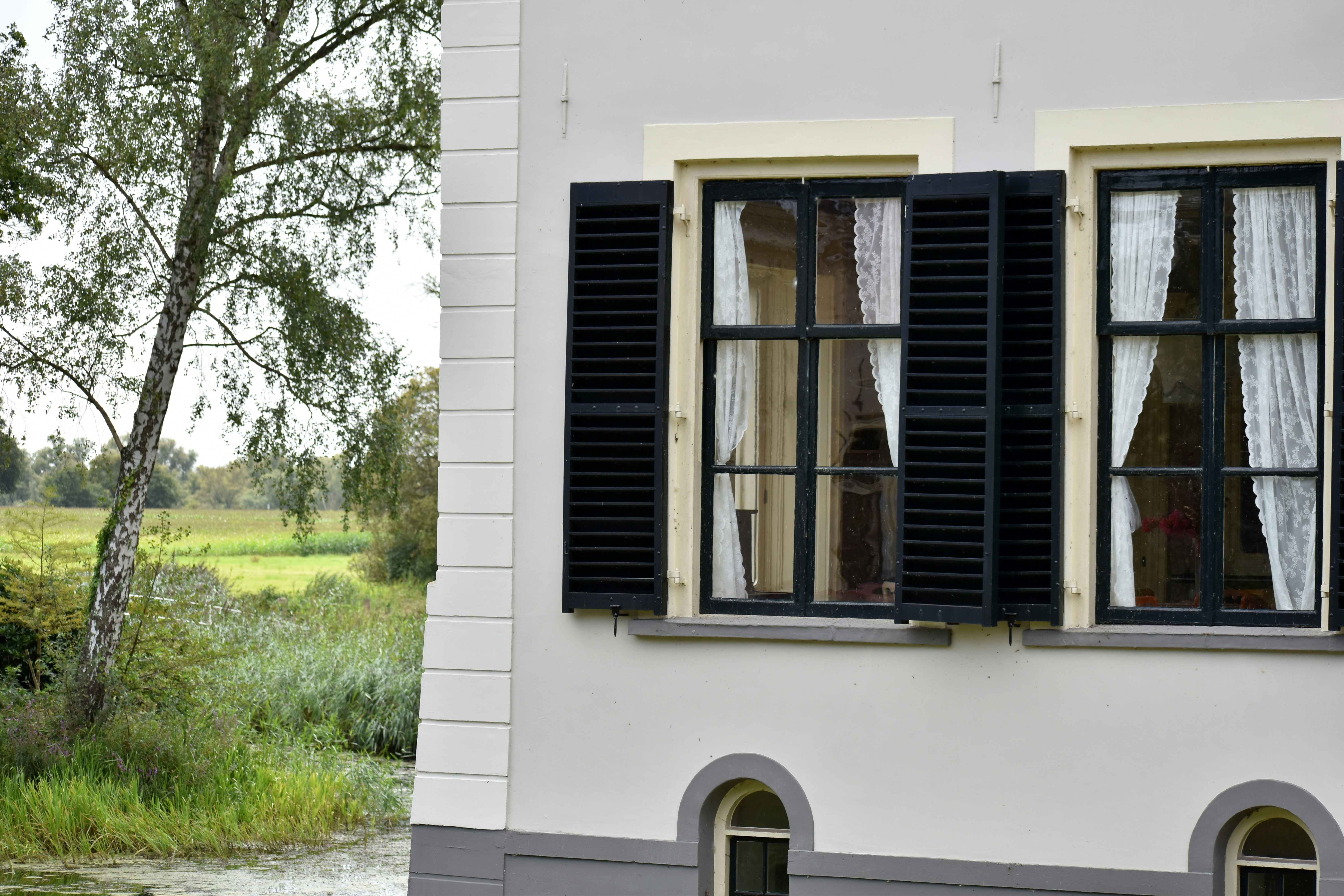 Classic Dutch architecture with black shutters and lace curtains beside a tranquil waterway.