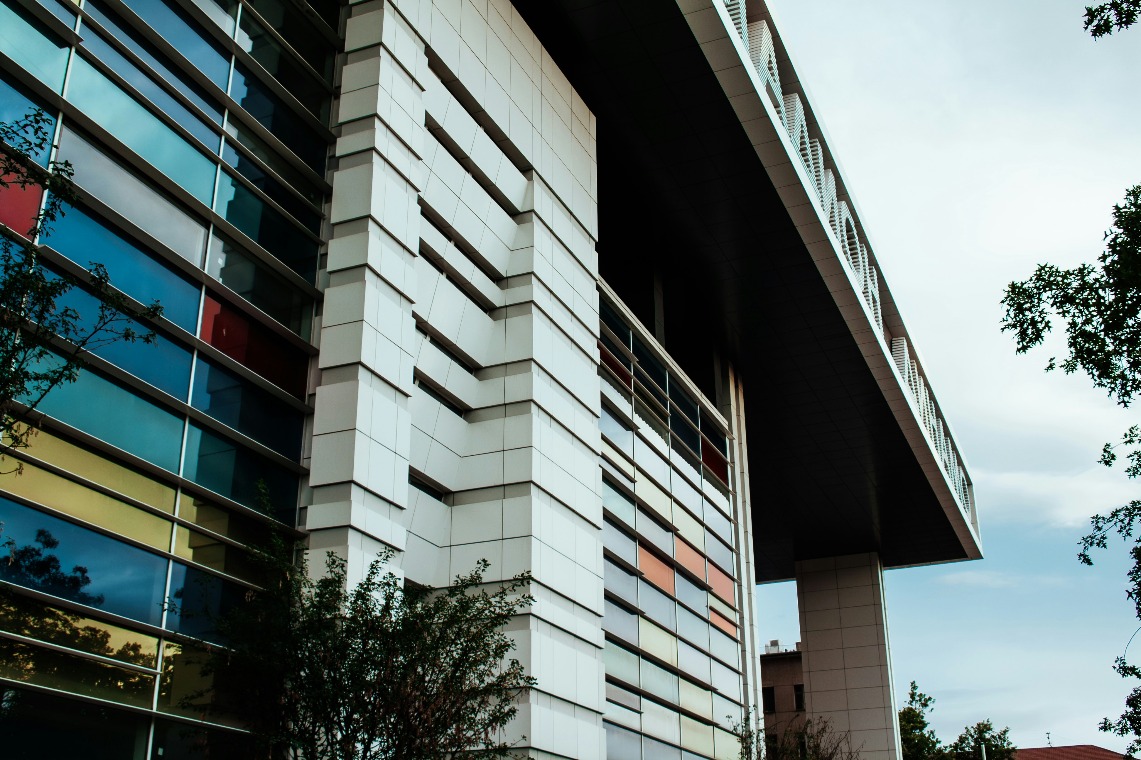 Modern building facade with colorful glass panels and geometric patterns against a cloudy sky.