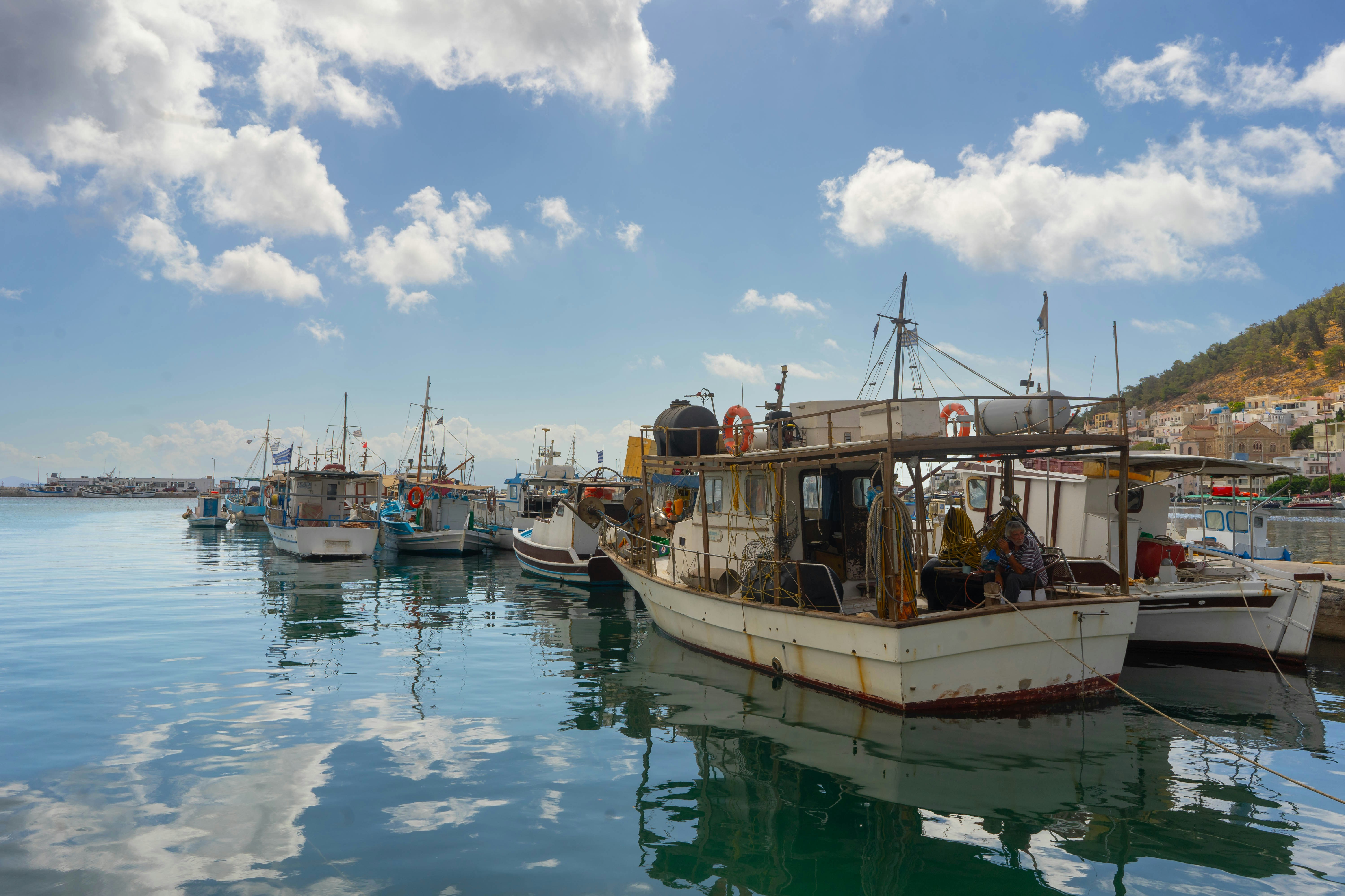 Fishing boats rest in a calm harbor under a vibrant blue sky with fluffy clouds.