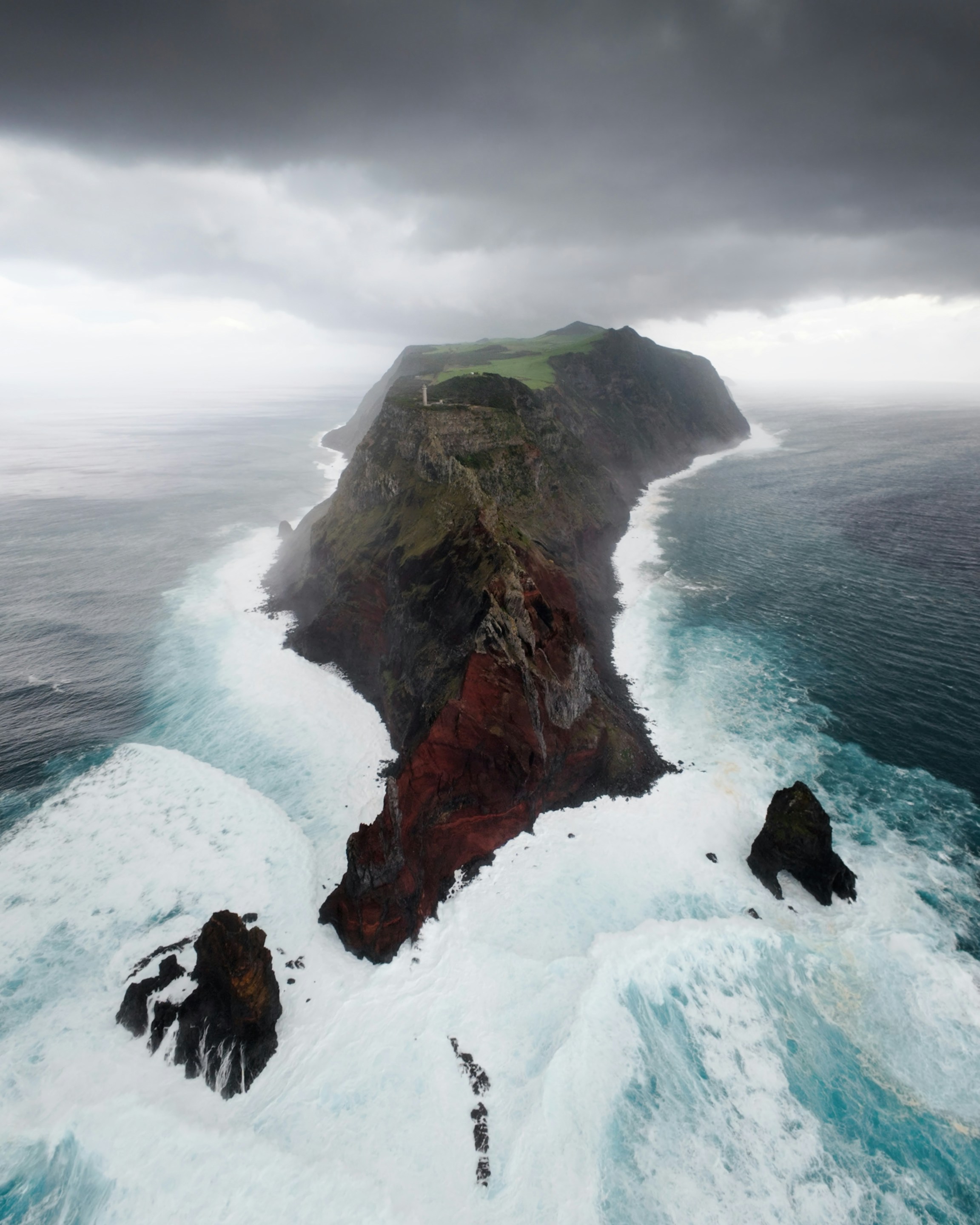 Rugged island cliffs surrounded by turbulent ocean waves under a stormy sky.