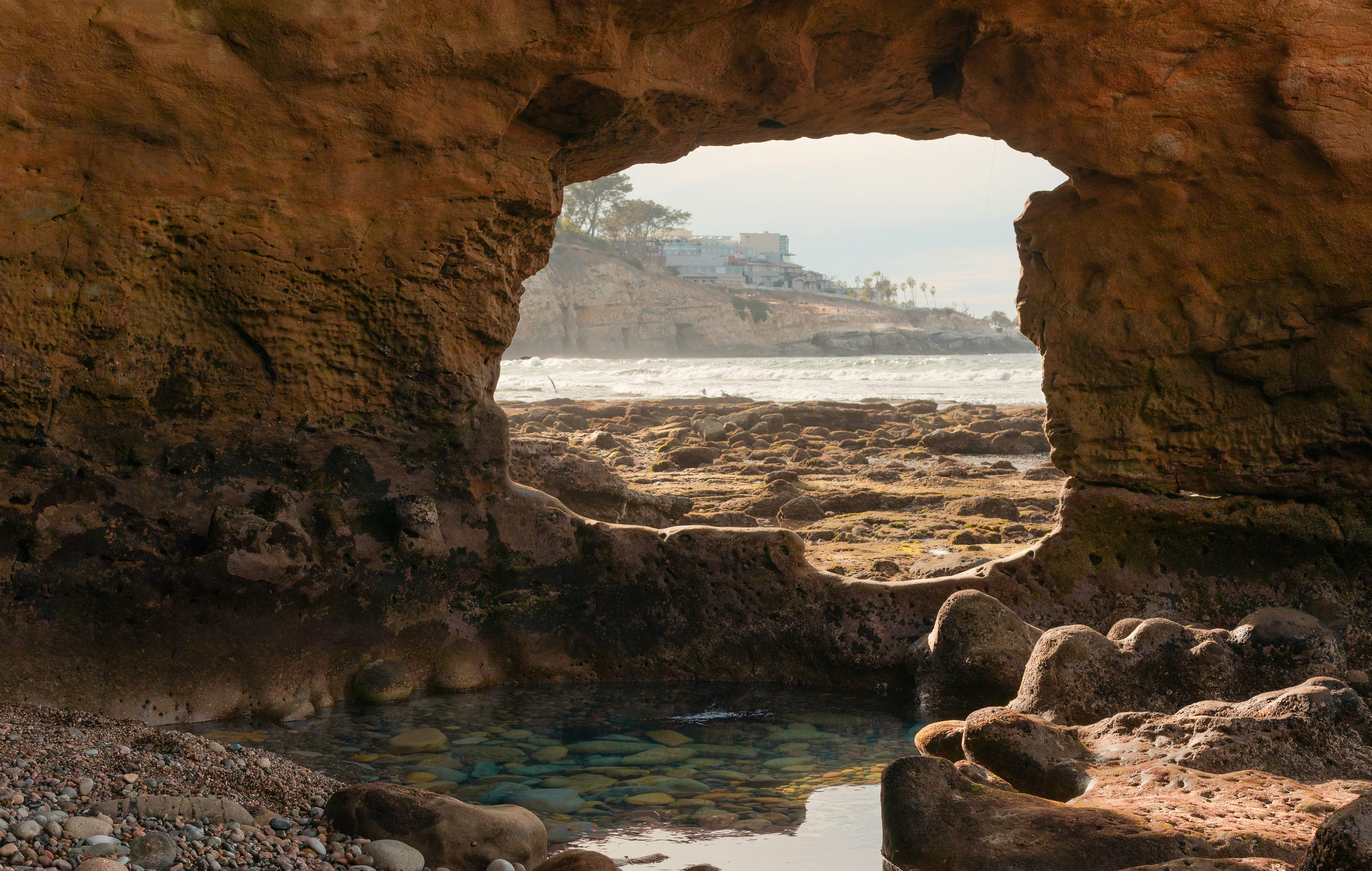 Natural rock arch frames a serene coastal scene with rugged rocks and gentle ocean waves.