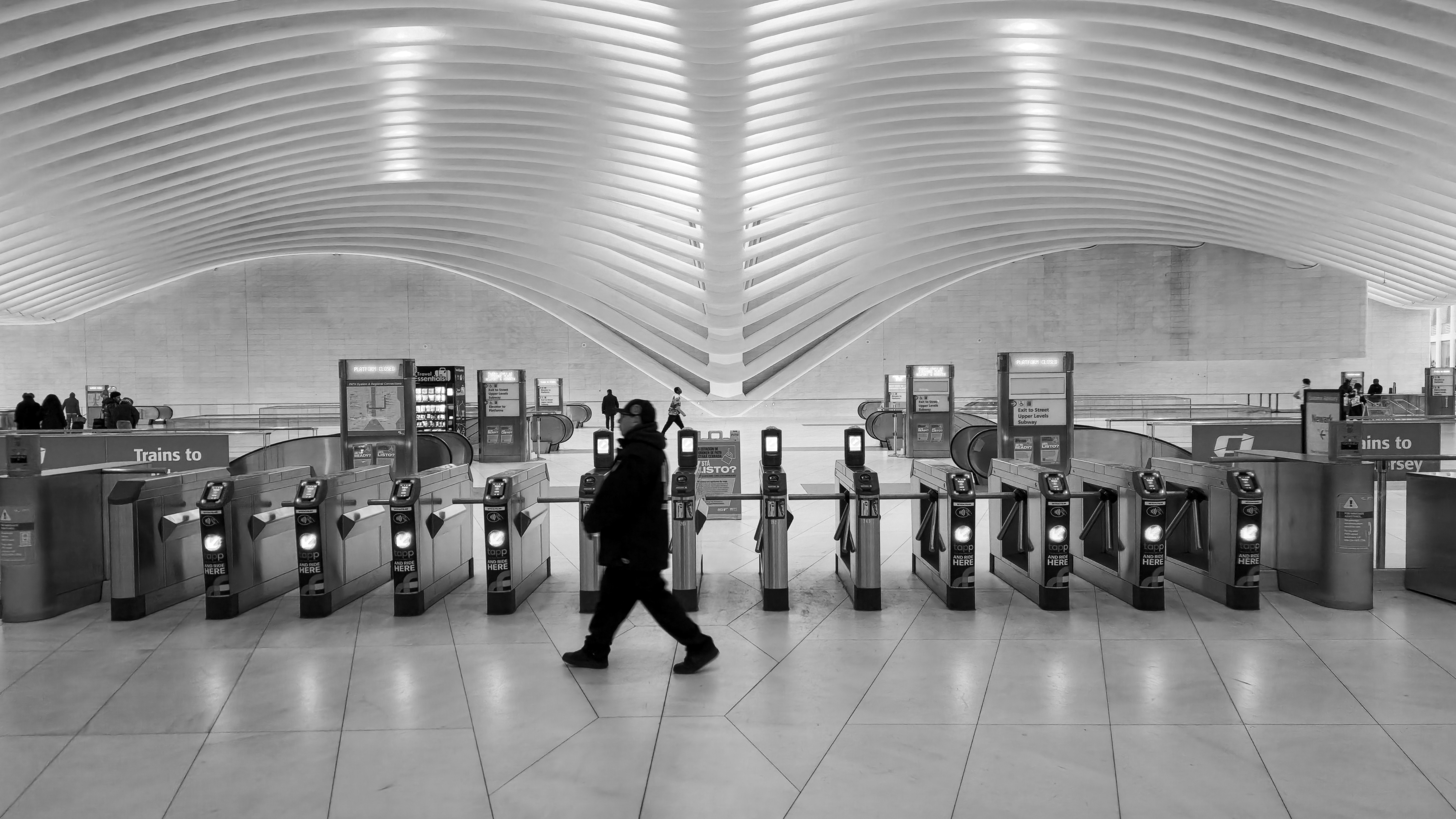Commuter strides through symmetrical turnstiles beneath ribbed architectural ceiling, creating dynamic movement.