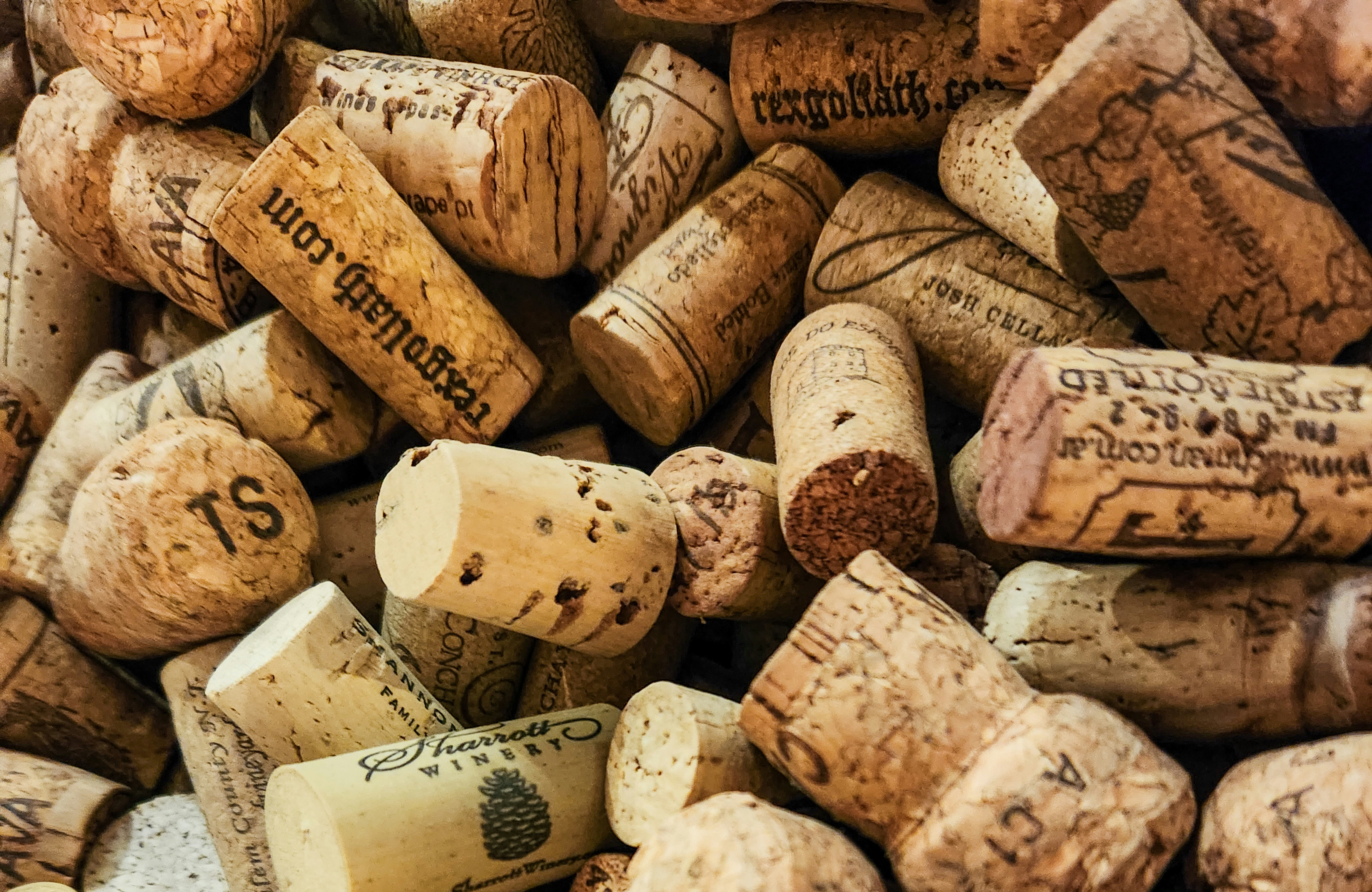 Wine corks piled together, showcasing varied typography and natural grain in warm, earthy tones.