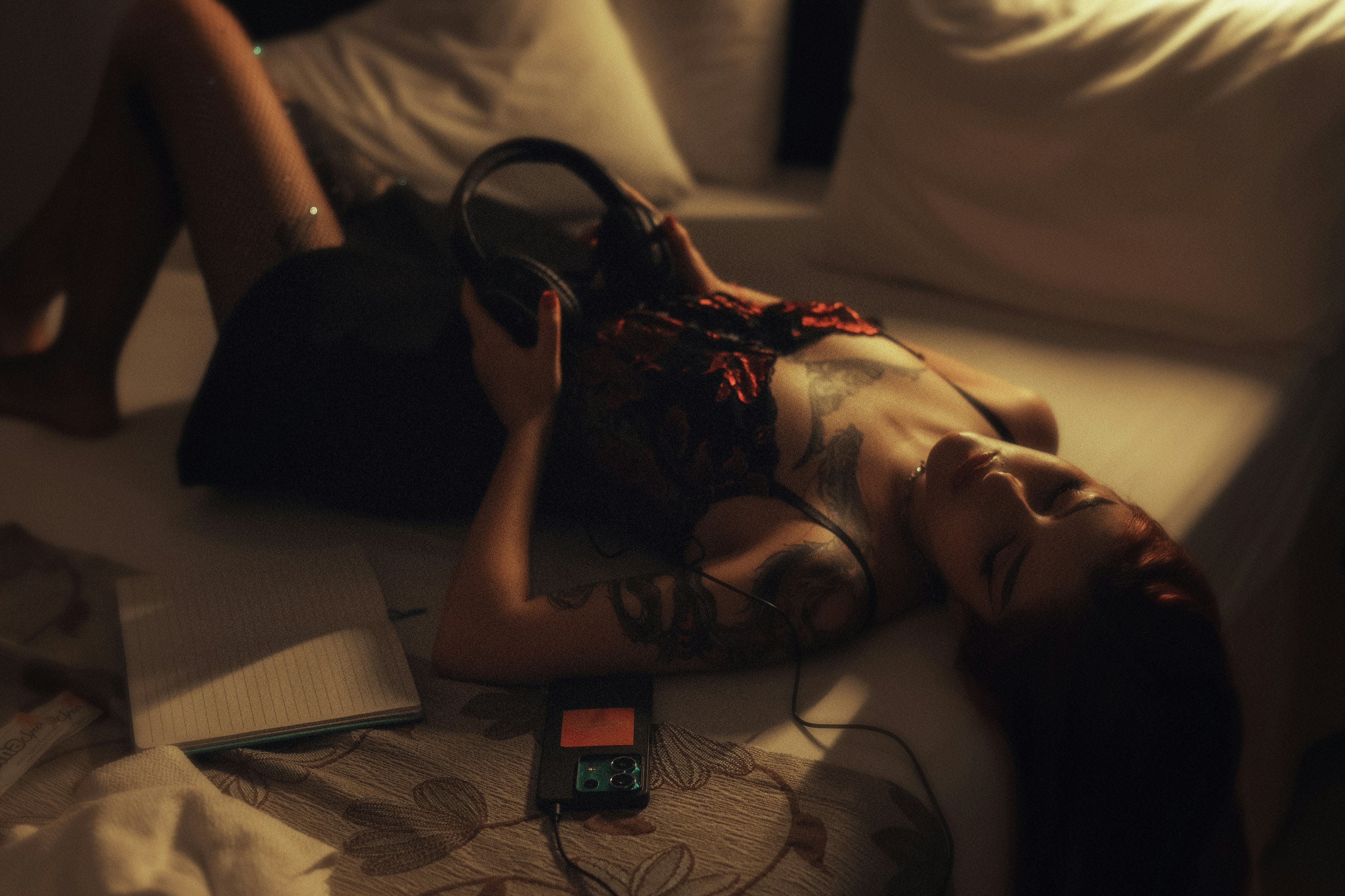 Moody photograph of a woman in lingerie lying on a bed, illuminated by warm ambient light; a small device with colorful lights rests near her.