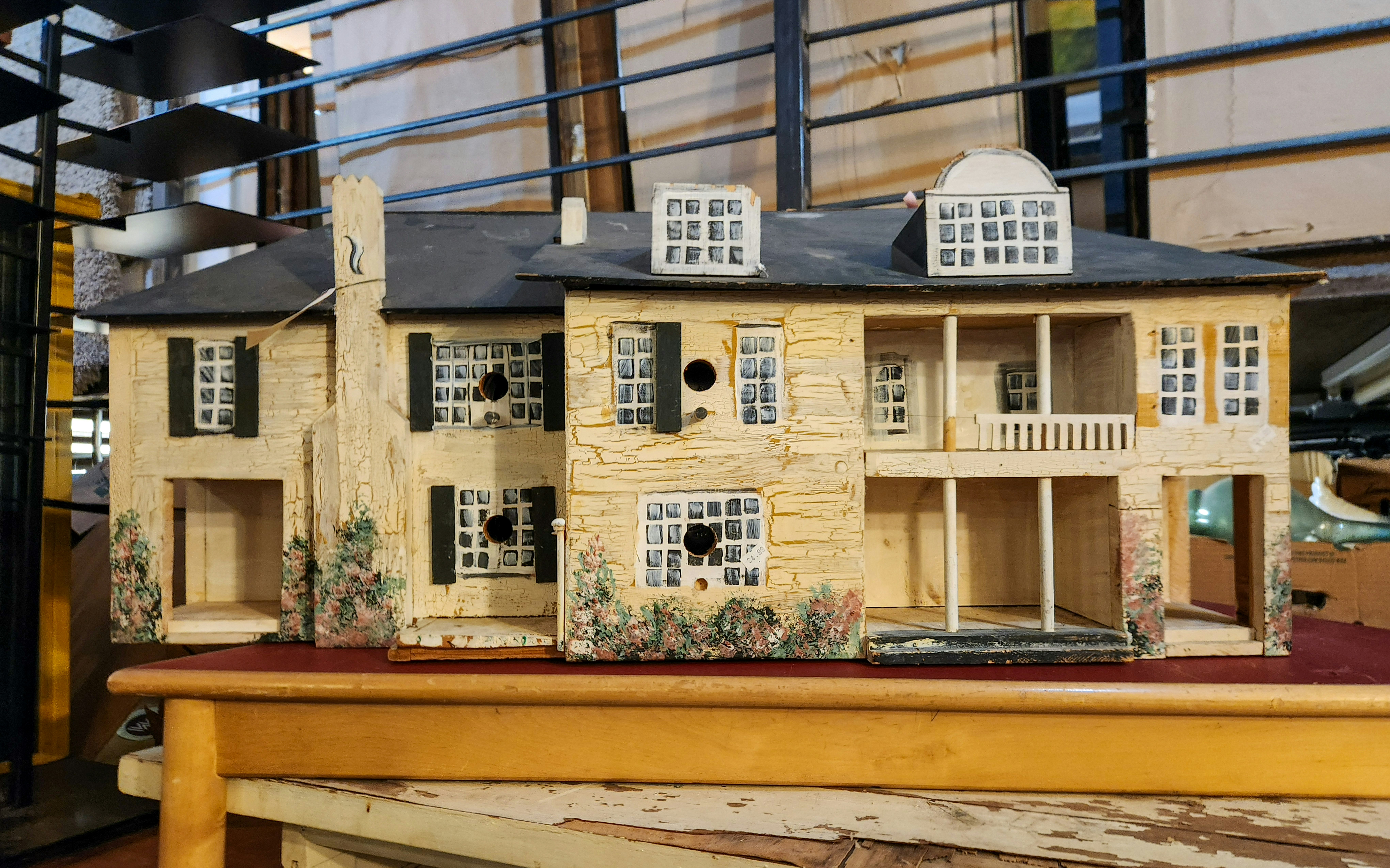 Intricately designed wooden dollhouse showcasing detailed windows and a charming facade, resting on a table in a workshop setting.
