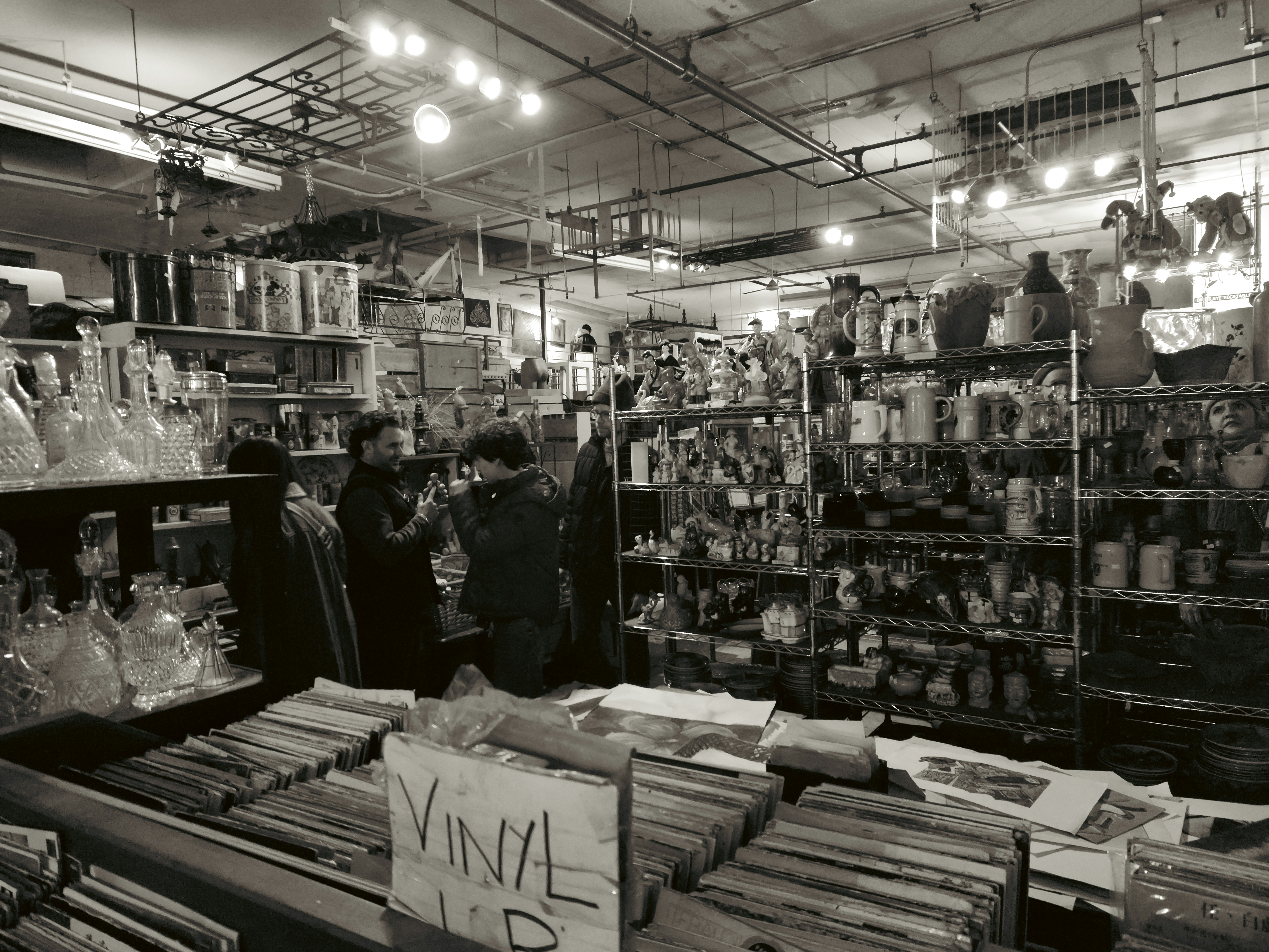 Black and white photo of people browsing an antique store filled with ceramics and vinyl records.