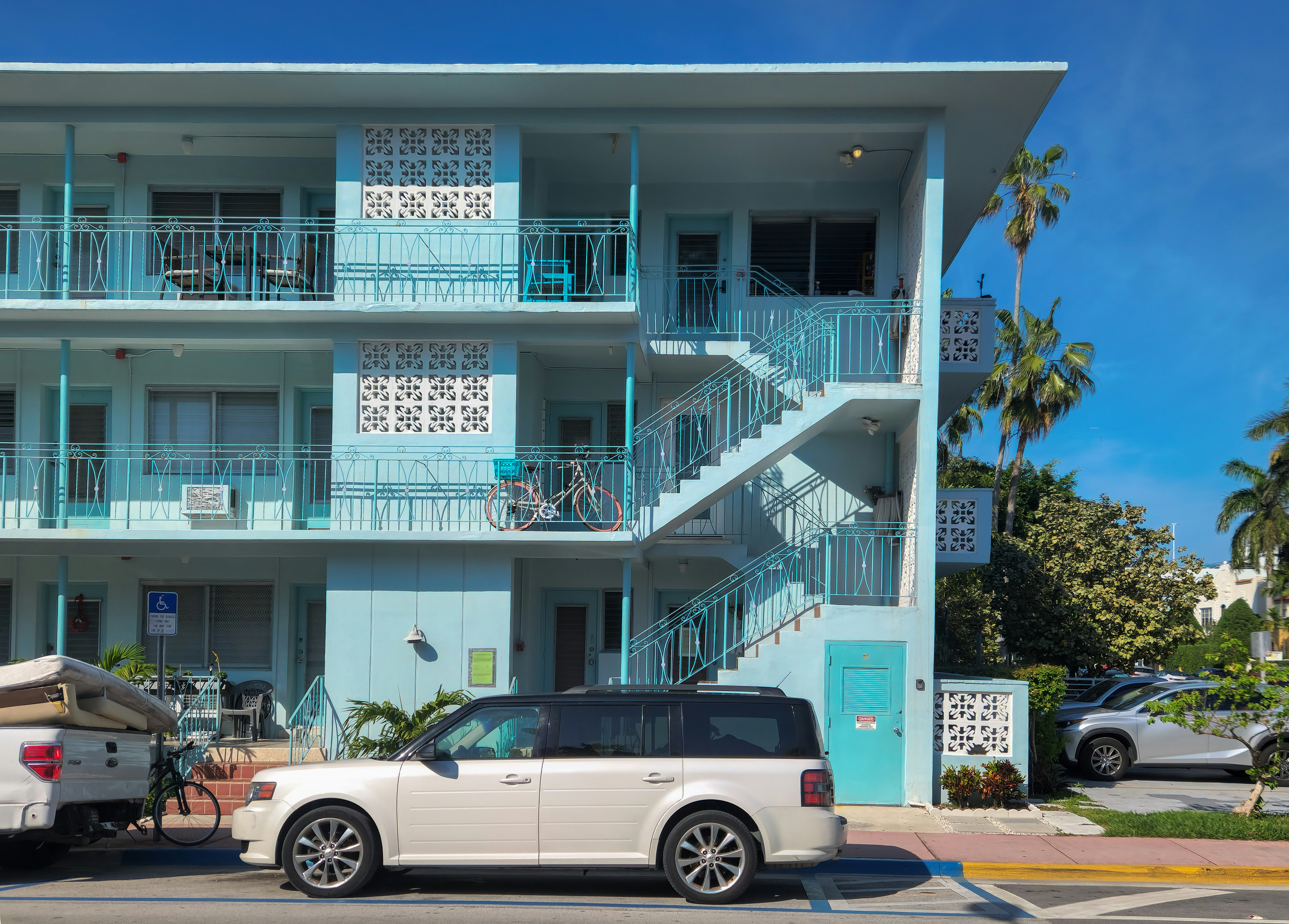 Retro building with turquoise facade, geometric railings, and vintage car under a clear blue sky.