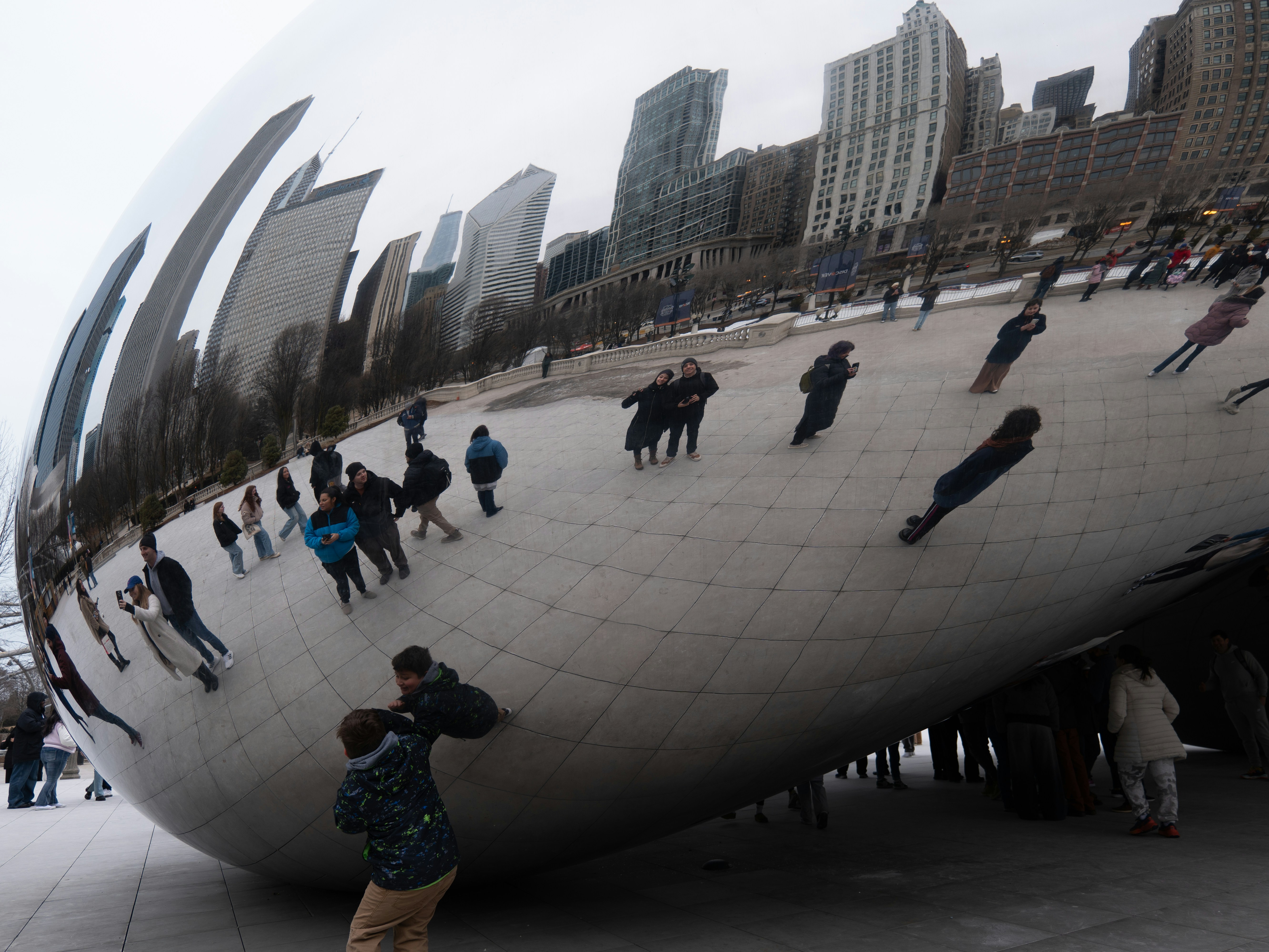 Cloud Gate sculpture in Chicago reflects surrounding skyscrapers and pedestrians under an overcast sky.