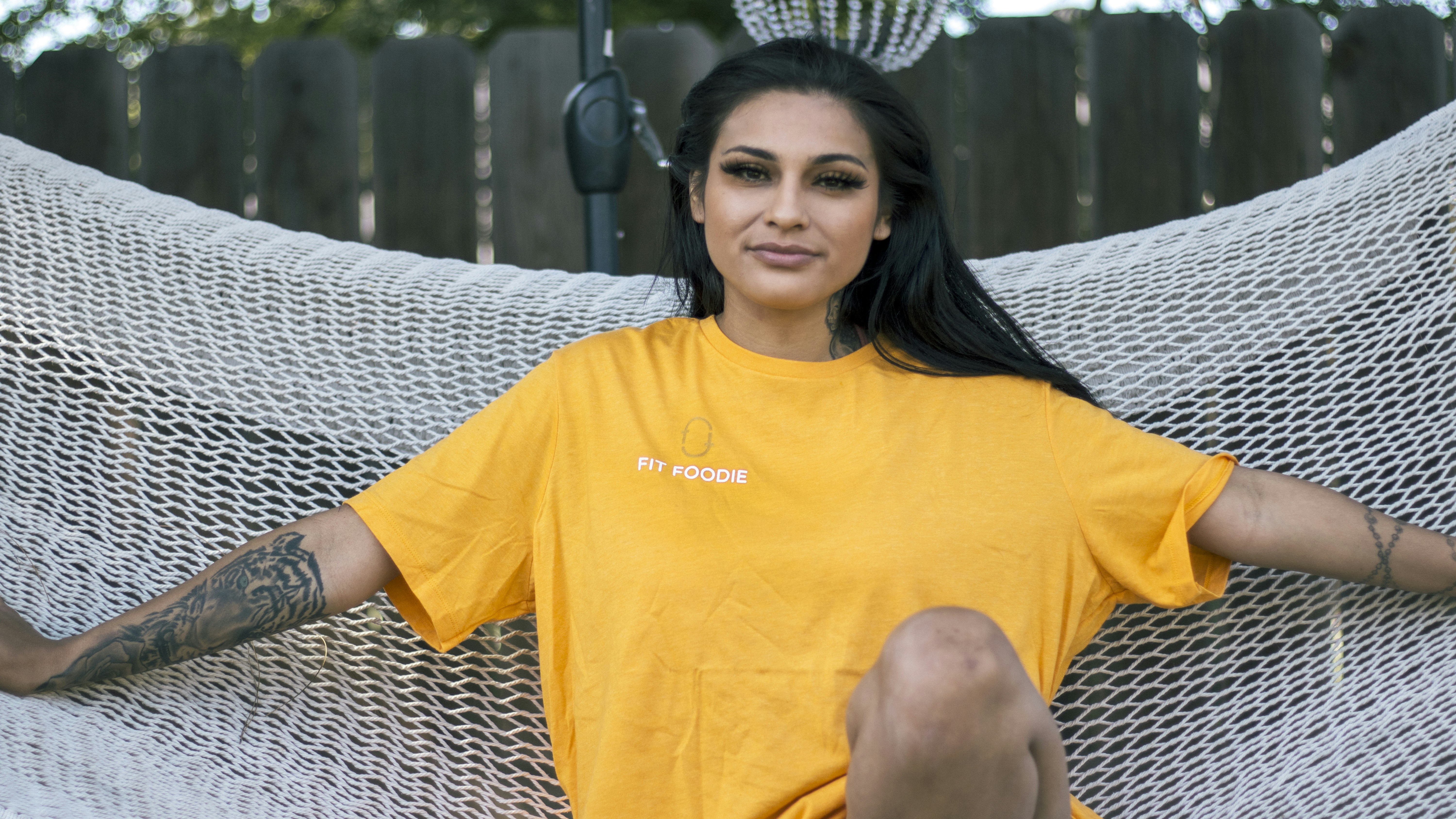 A woman in a bright yellow shirt lounges comfortably in a hammock, surrounded by a serene outdoor setting.