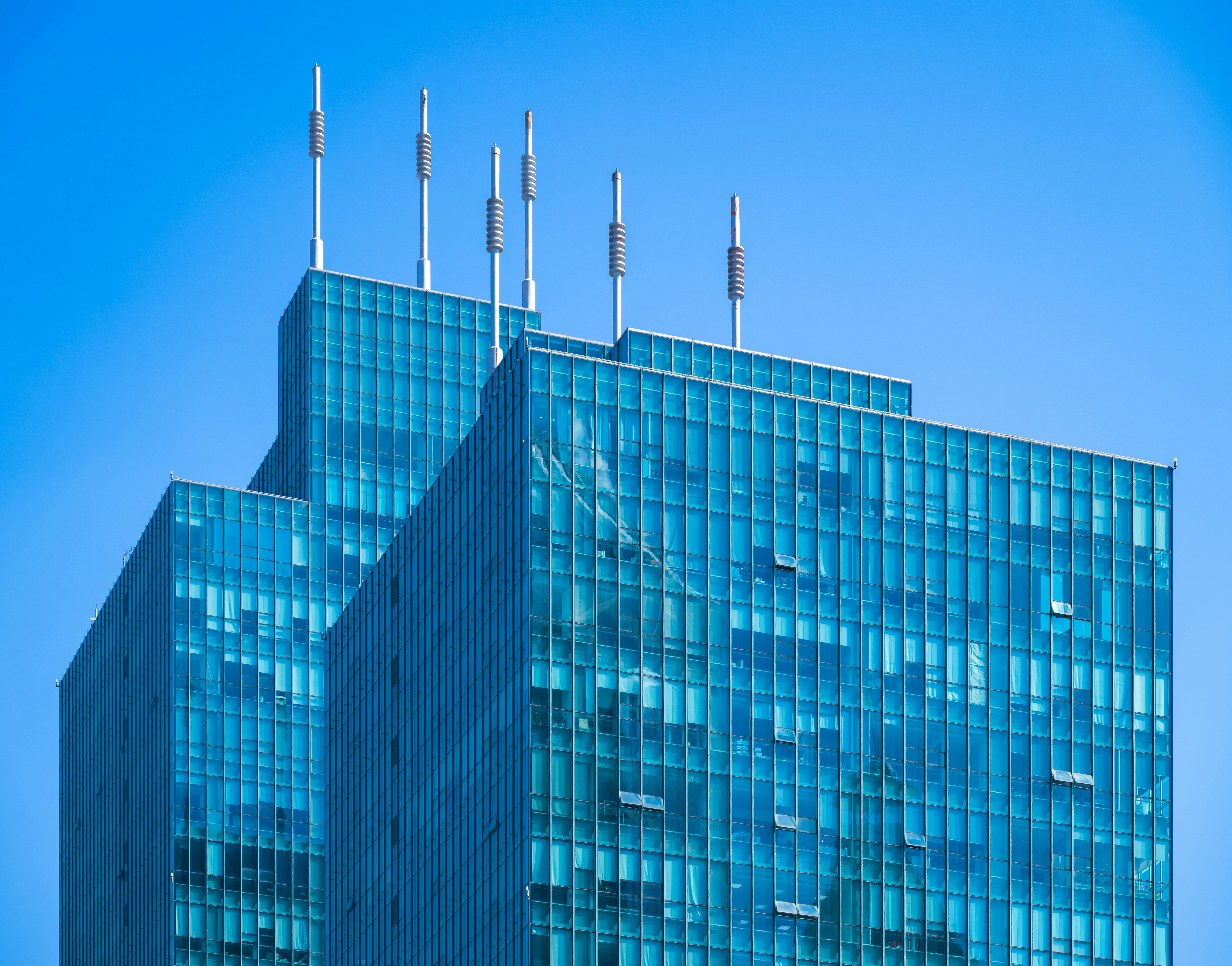 Modern skyscraper with reflective blue glass facade against a vibrant clear sky, showcasing geometric symmetry and natural light play.