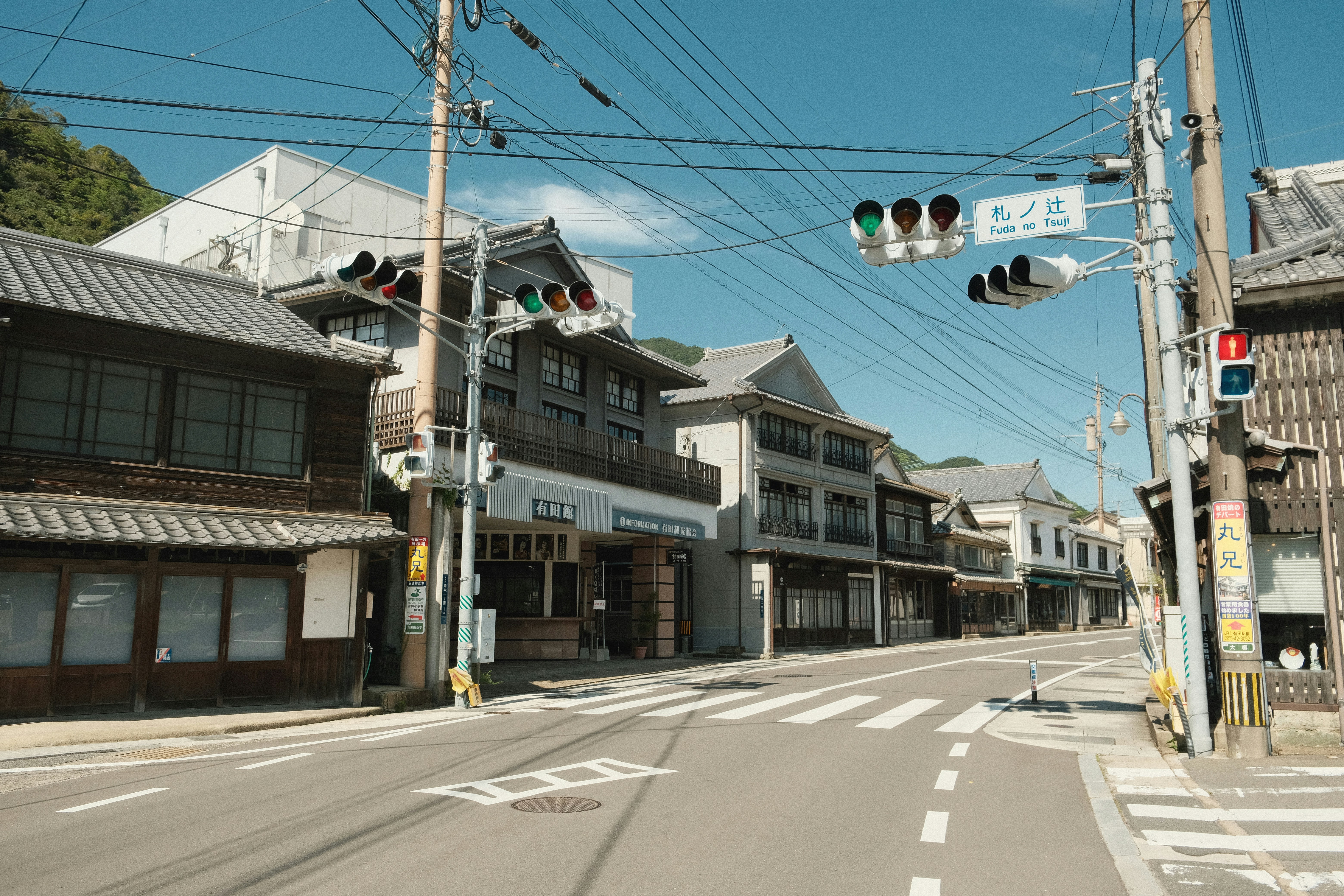 Serene street in a historic Japanese town with traditional wooden buildings and intricate power lines under a clear blue sky.