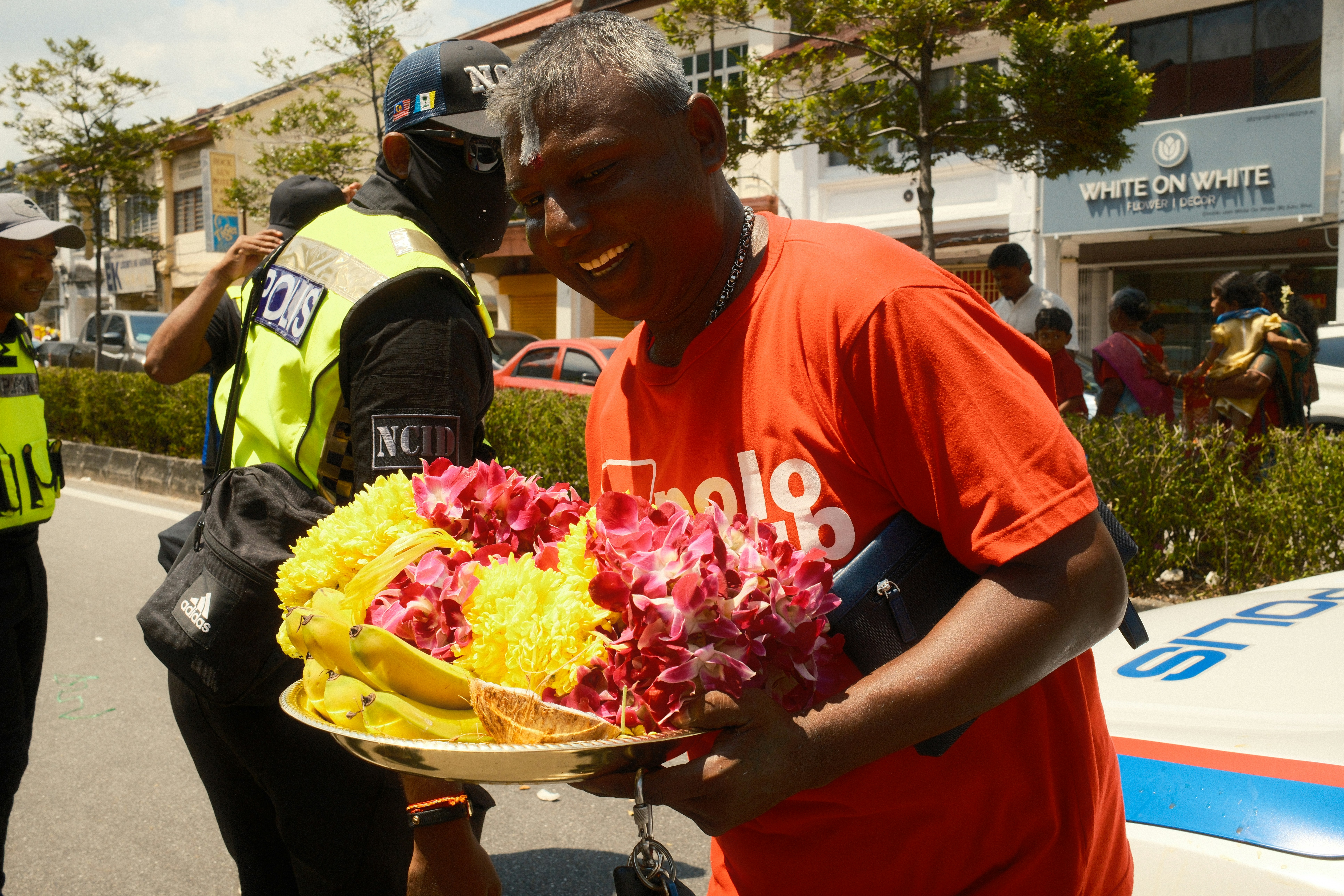 Bouquet of smiles: a person in red shirt presents flowers beside a police escort