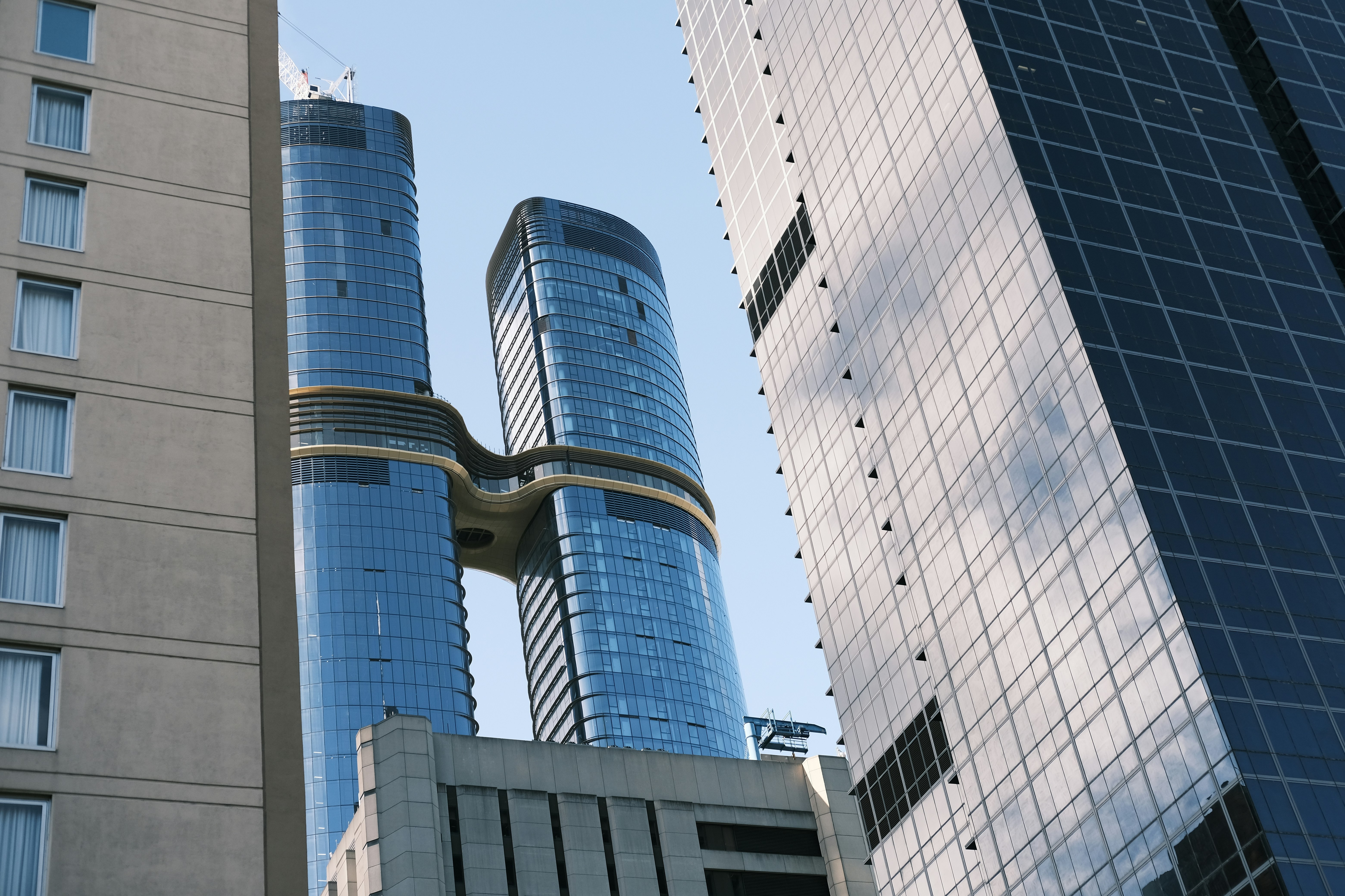 Cylindrical glass towers framed by skyscrapers under a clear blue sky.
