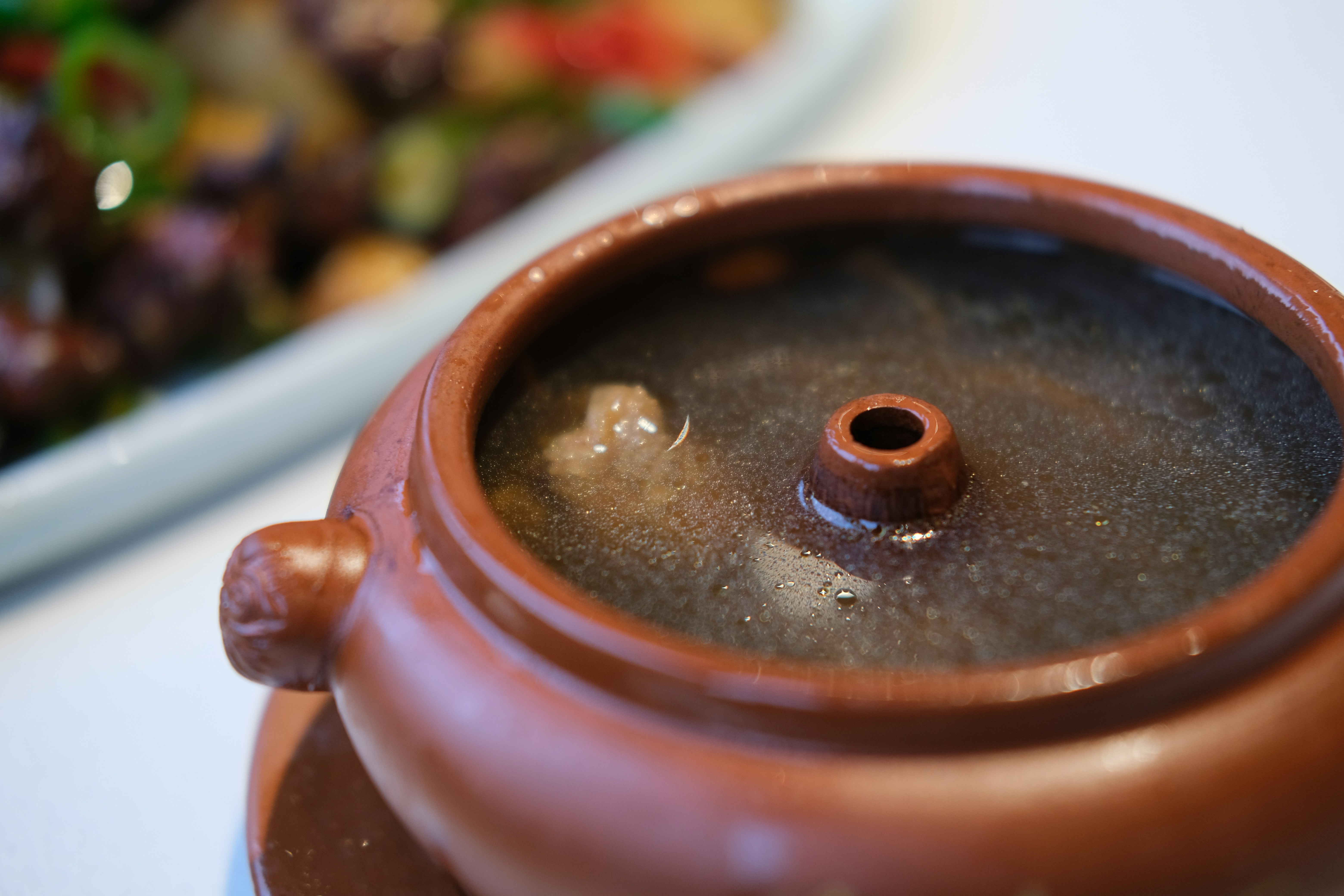 Rustic clay pot with steaming broth, contrasting with a vibrant, blurred background.
