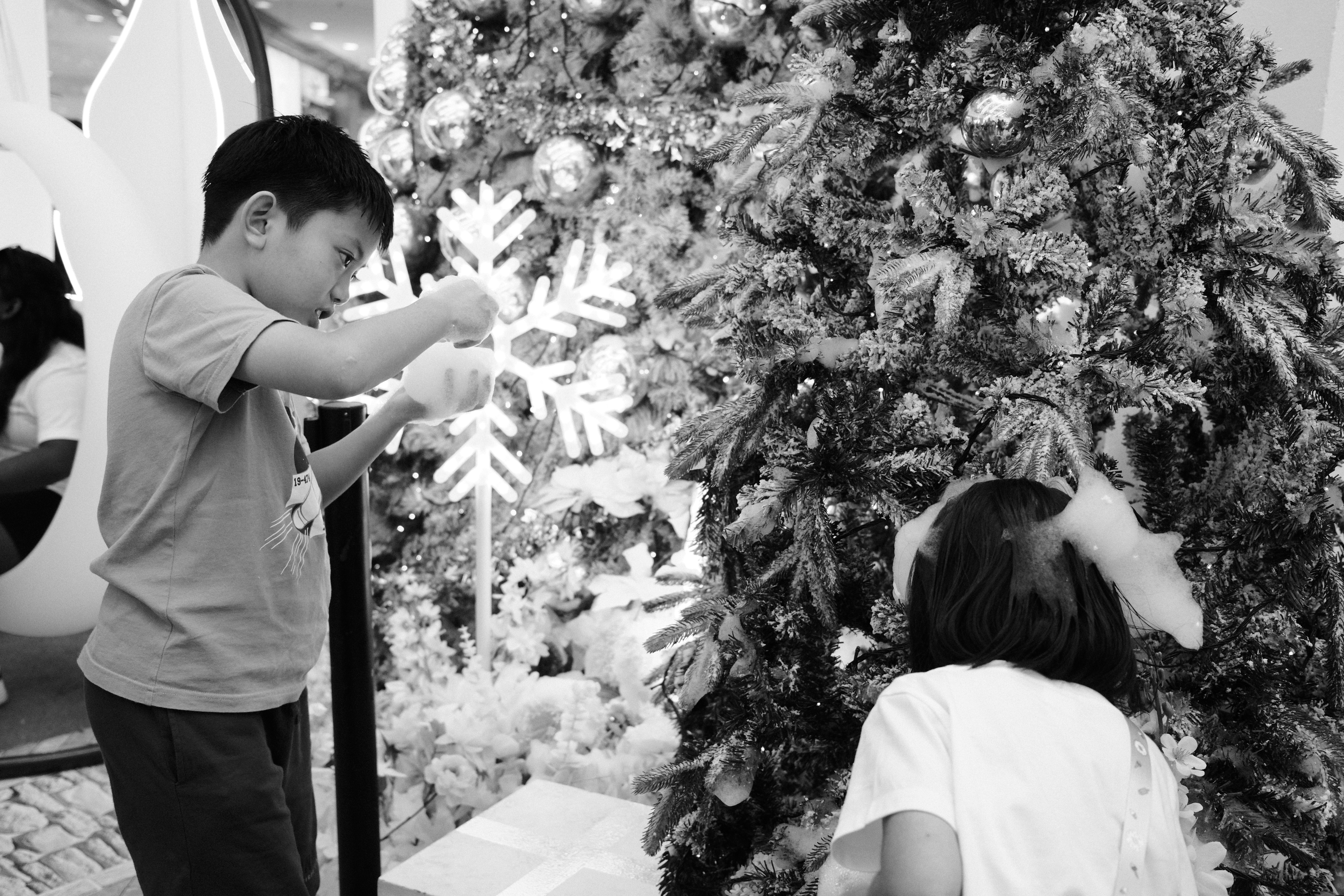 Children decorating a Christmas tree with festive ornaments and a glowing snowflake. Soft lighting accentuates the scene's whimsical atmosphere.