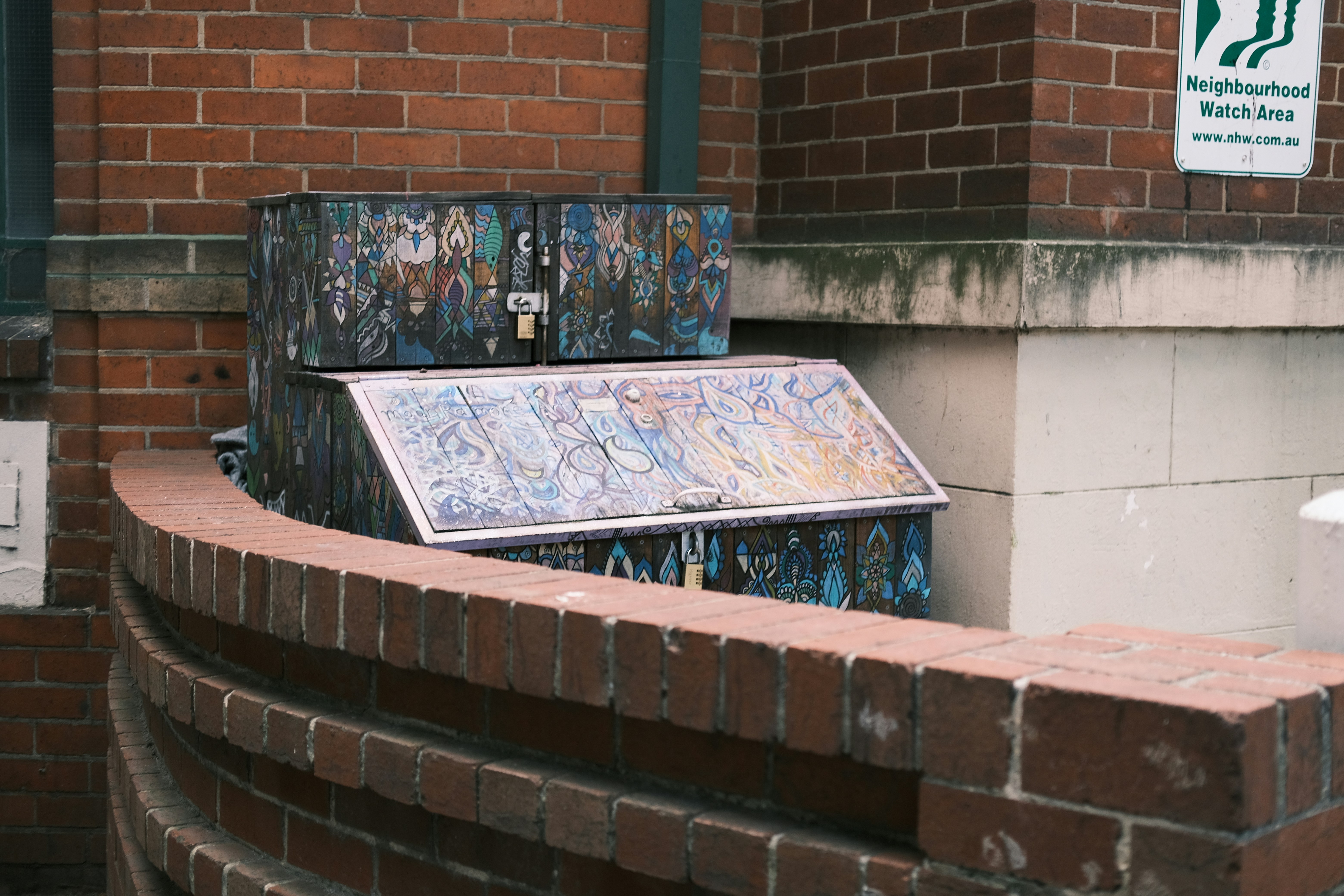 Street art on utility boxes with vibrant blues and purples contrasts against red brick walls.