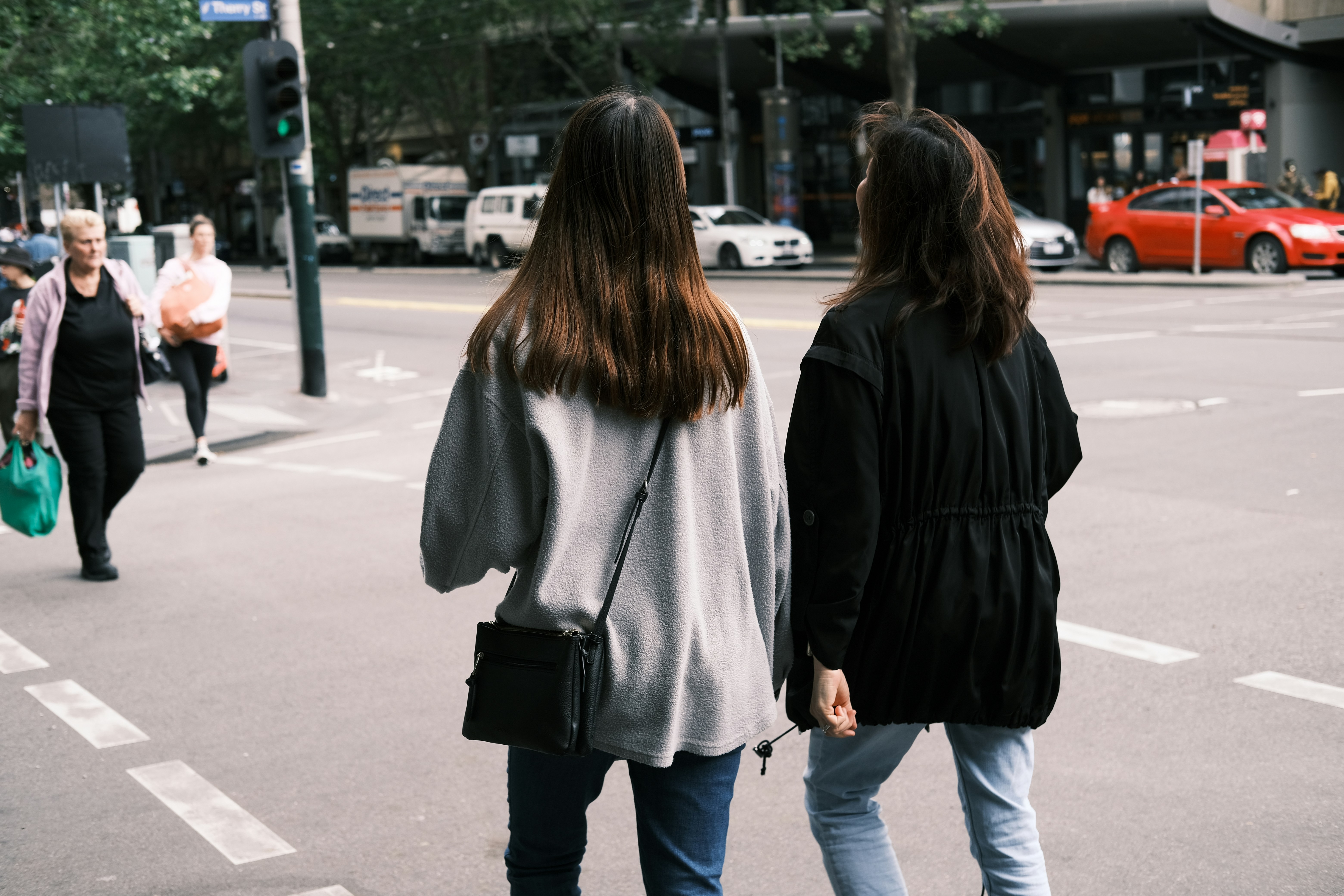 Two individuals walk through a busy city intersection with vibrant cars in the background, highlighting urban life.