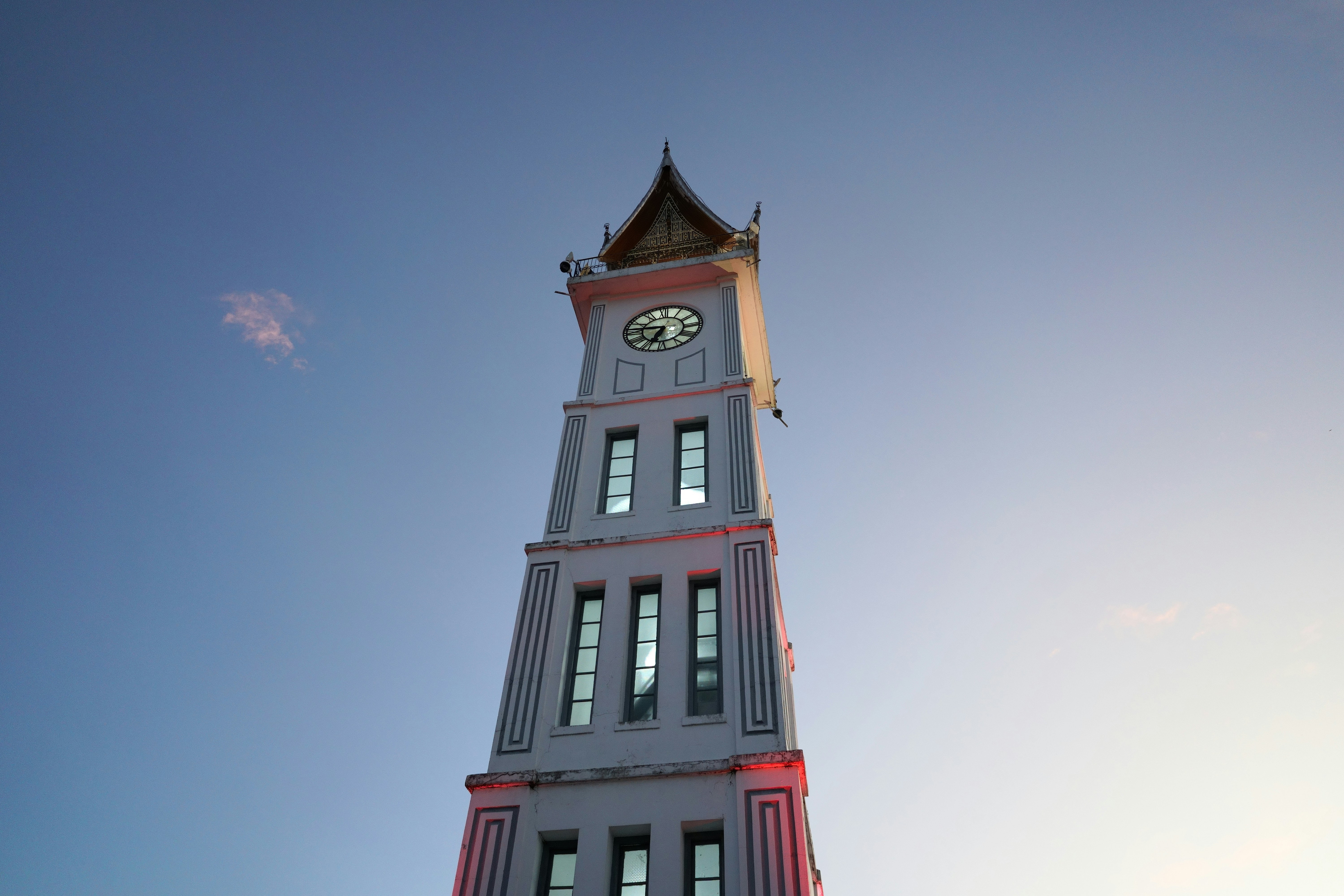 Tall clock tower silhouetted against a clear twilight sky with red accents and architectural details highlighted by soft evening light.