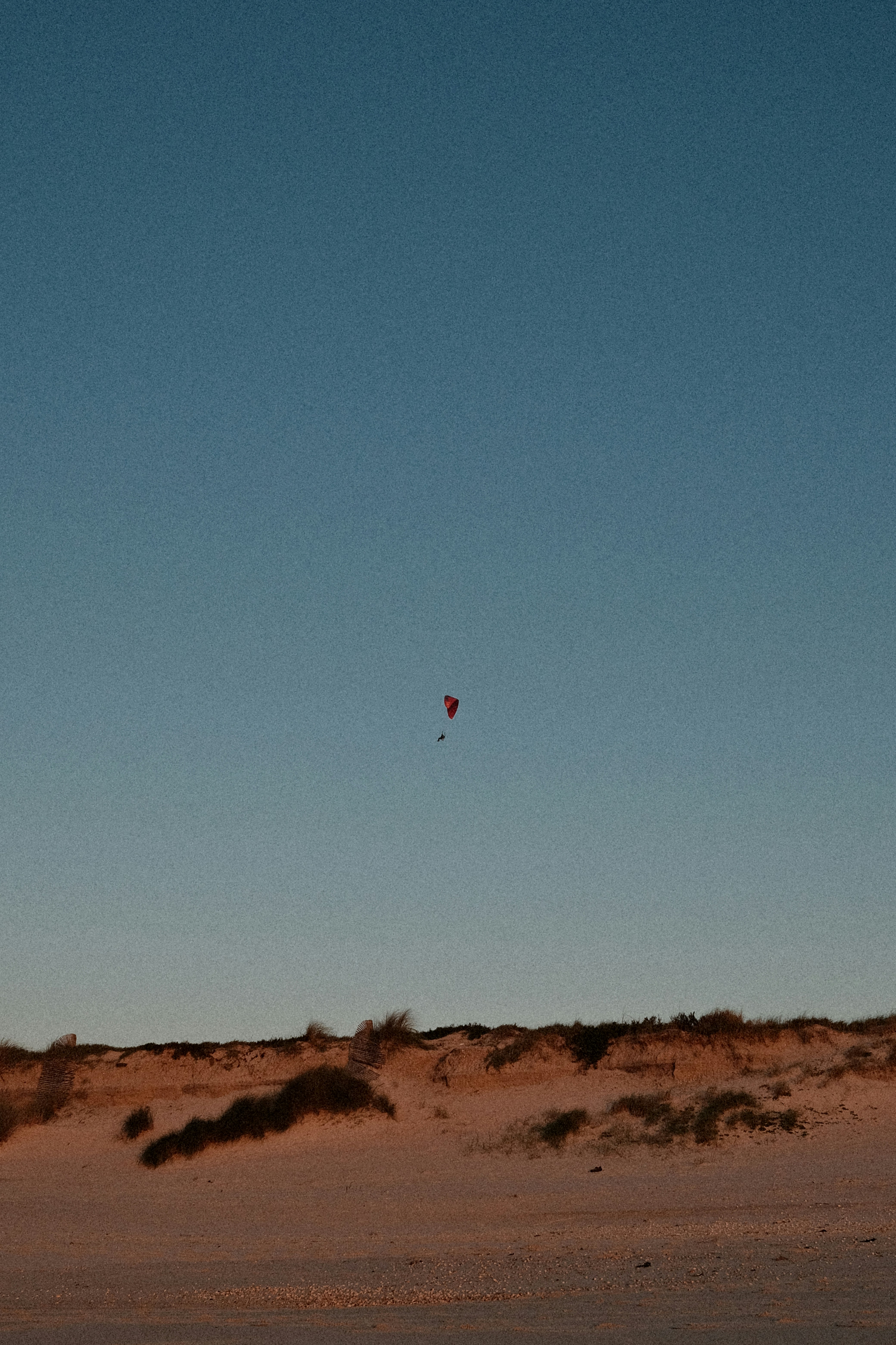 Crimson Paraglider Skimming the Desert's Quiet Horizon